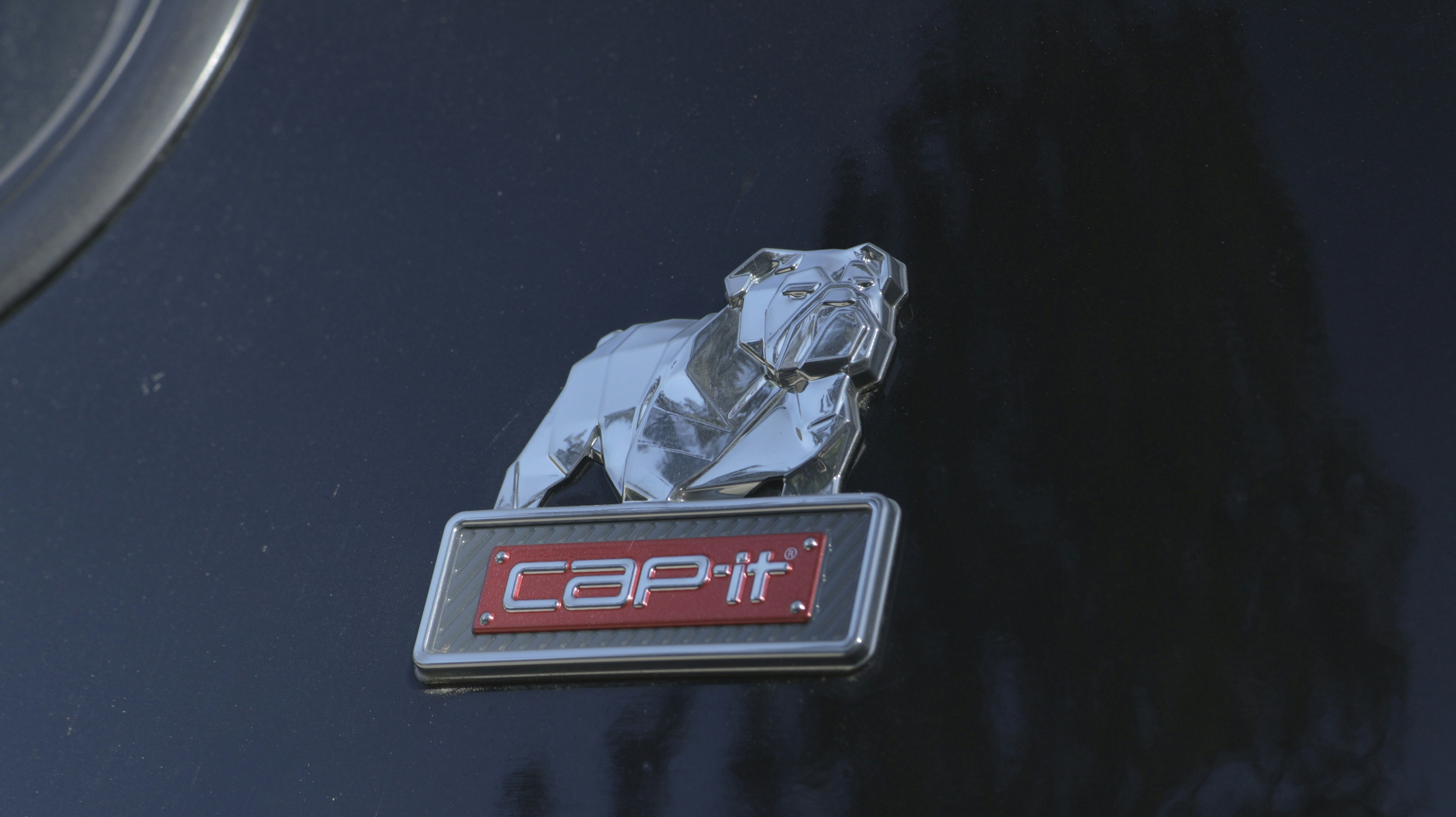 Foiled Accent: Close-up of the Cap-It Chrome Badge on a Dark Car Hood