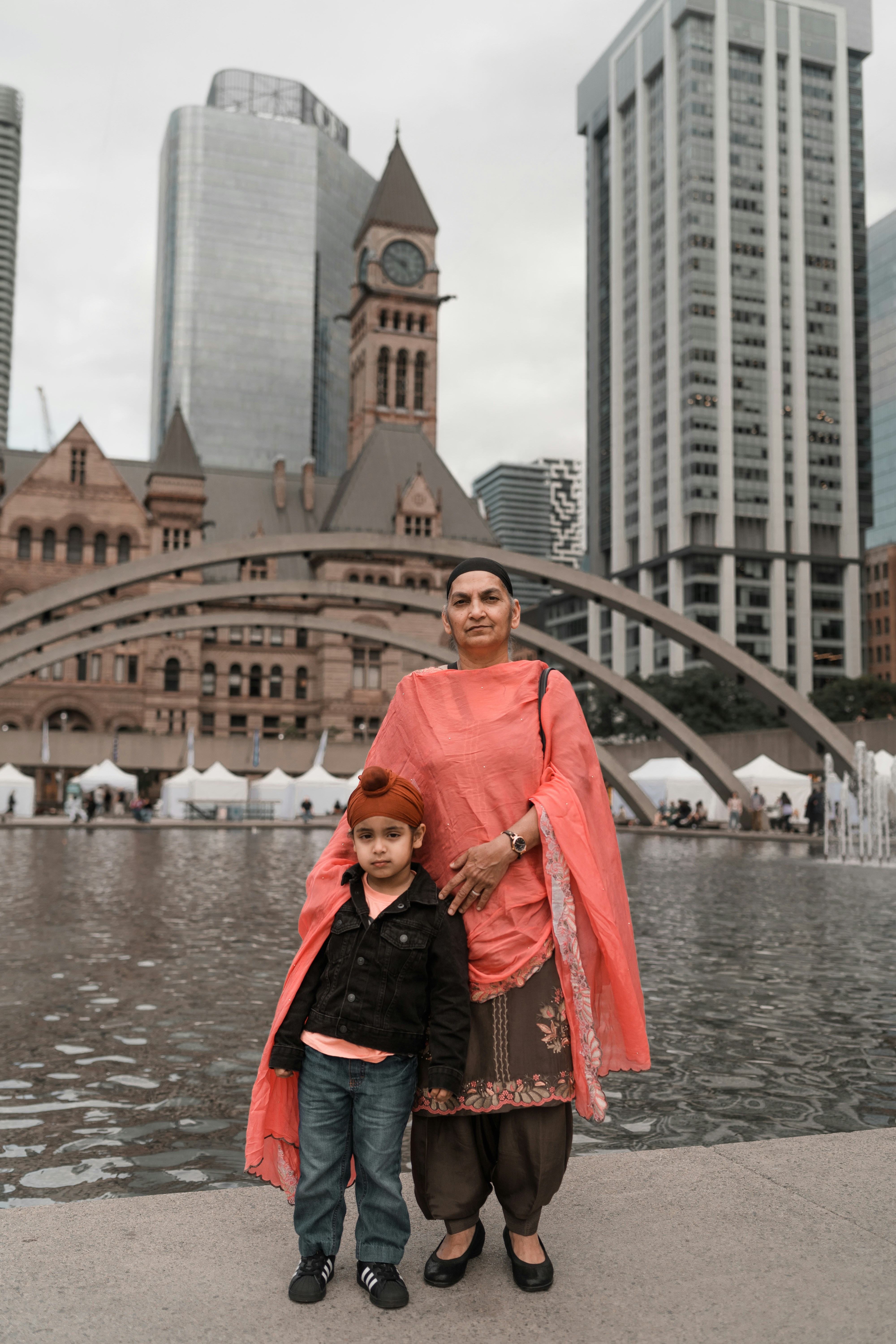 Coral Cloaks by the Fountain: A Mother and Daughter Under the City Arch
