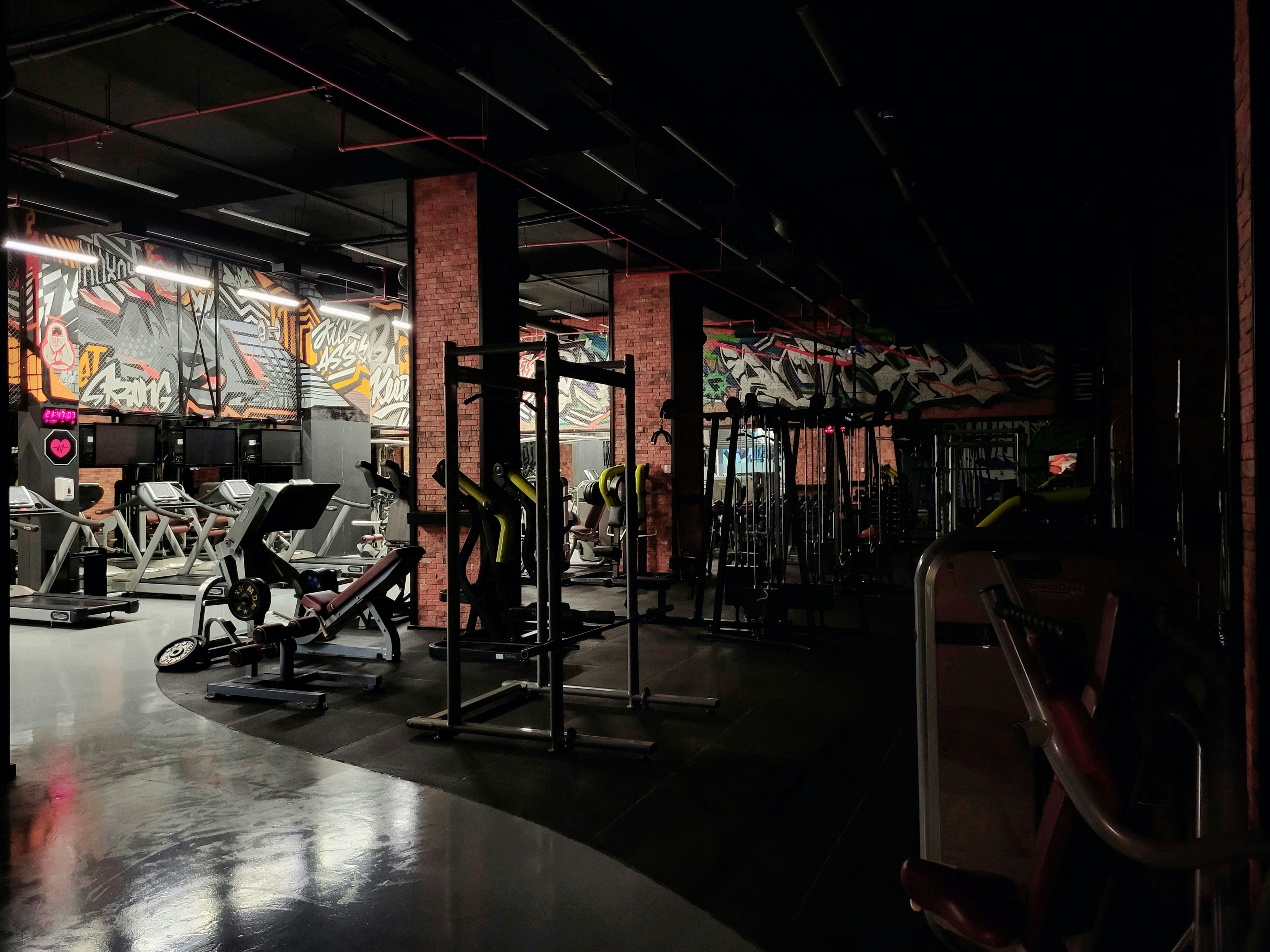 Dimly lit gym interior featuring workout equipment and vibrant graffiti murals on the walls.