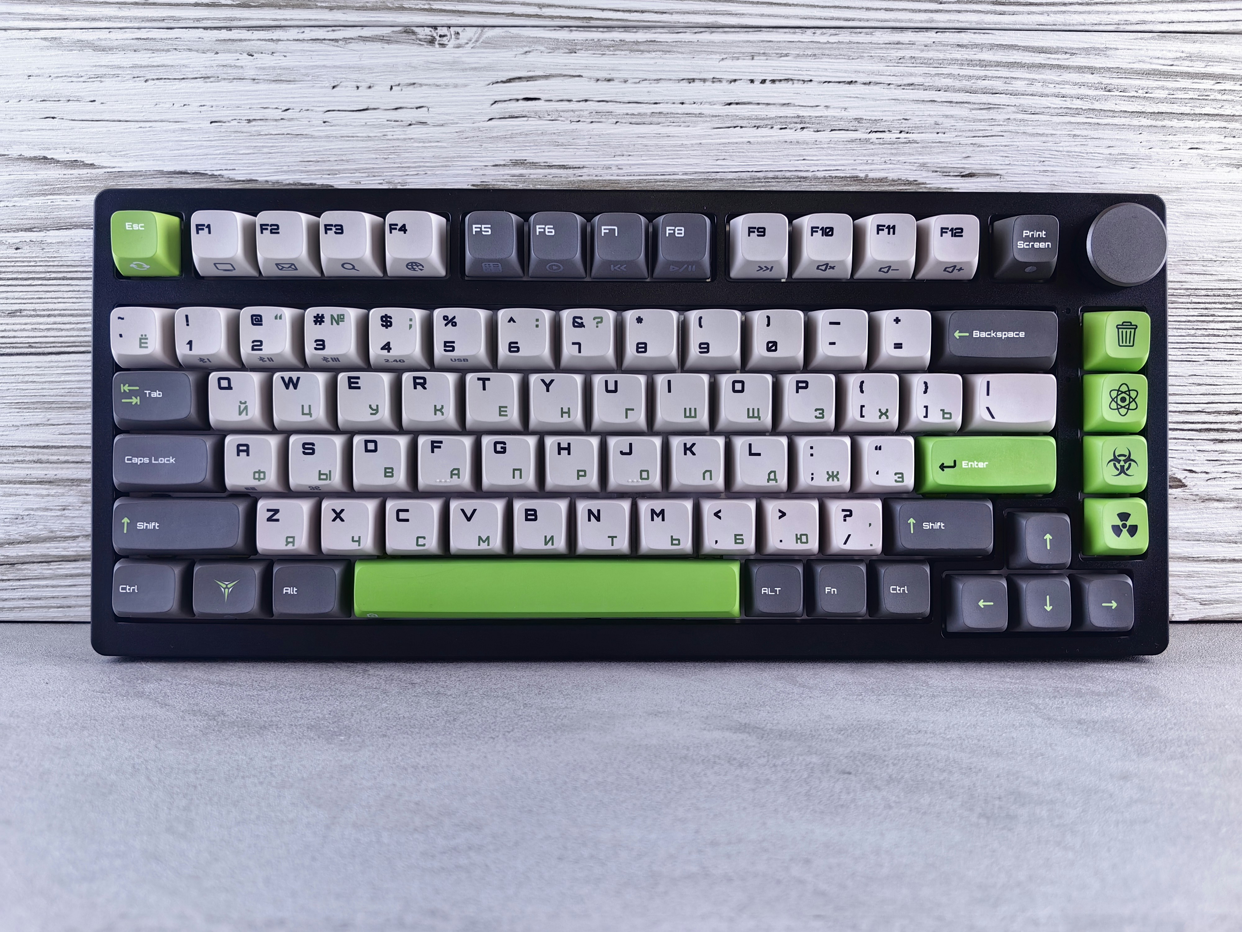 Compact mechanical keyboard with gray and lime-green keys sits on a light wood surface. The lime-green accents highlight the keyboard's design.