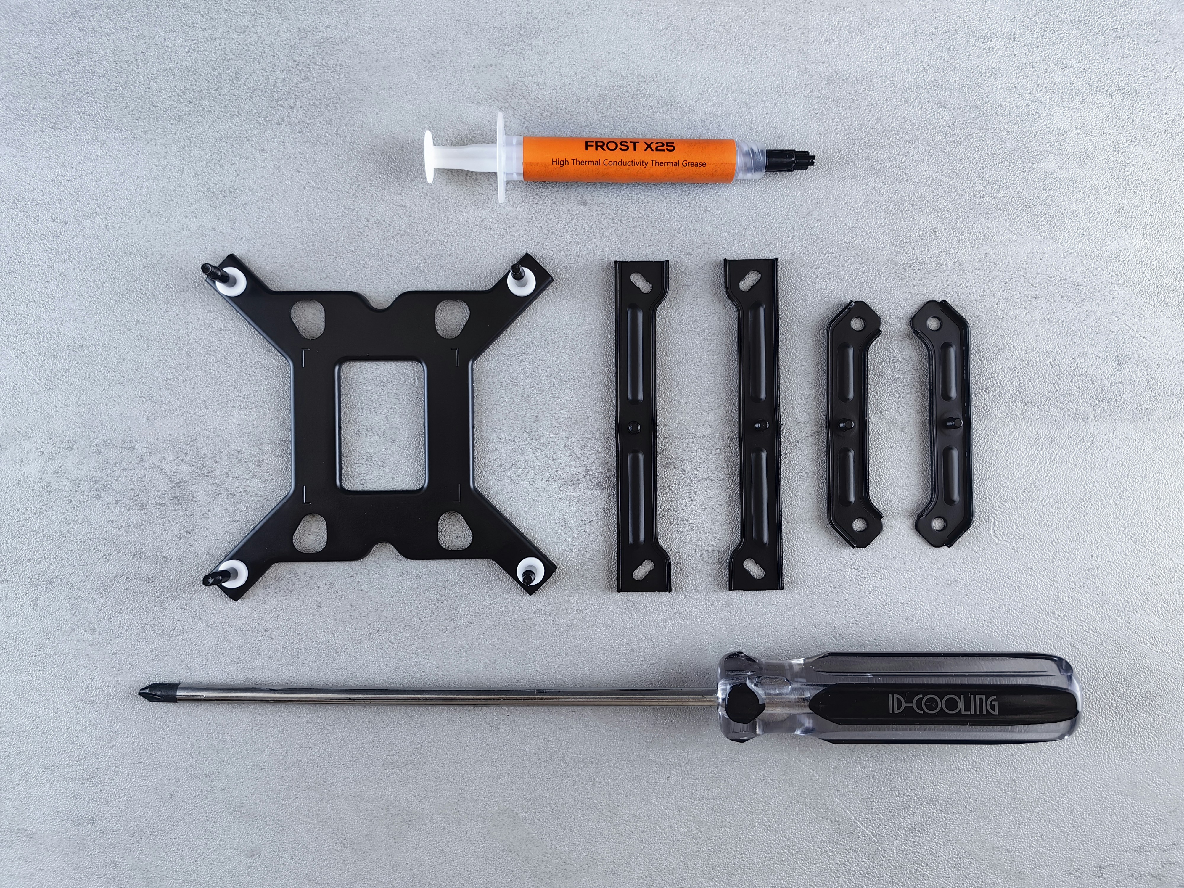 A layout of essential computer cooling installation components, including a mounting bracket, thermal paste, and a screwdriver, arranged on a smooth surface.