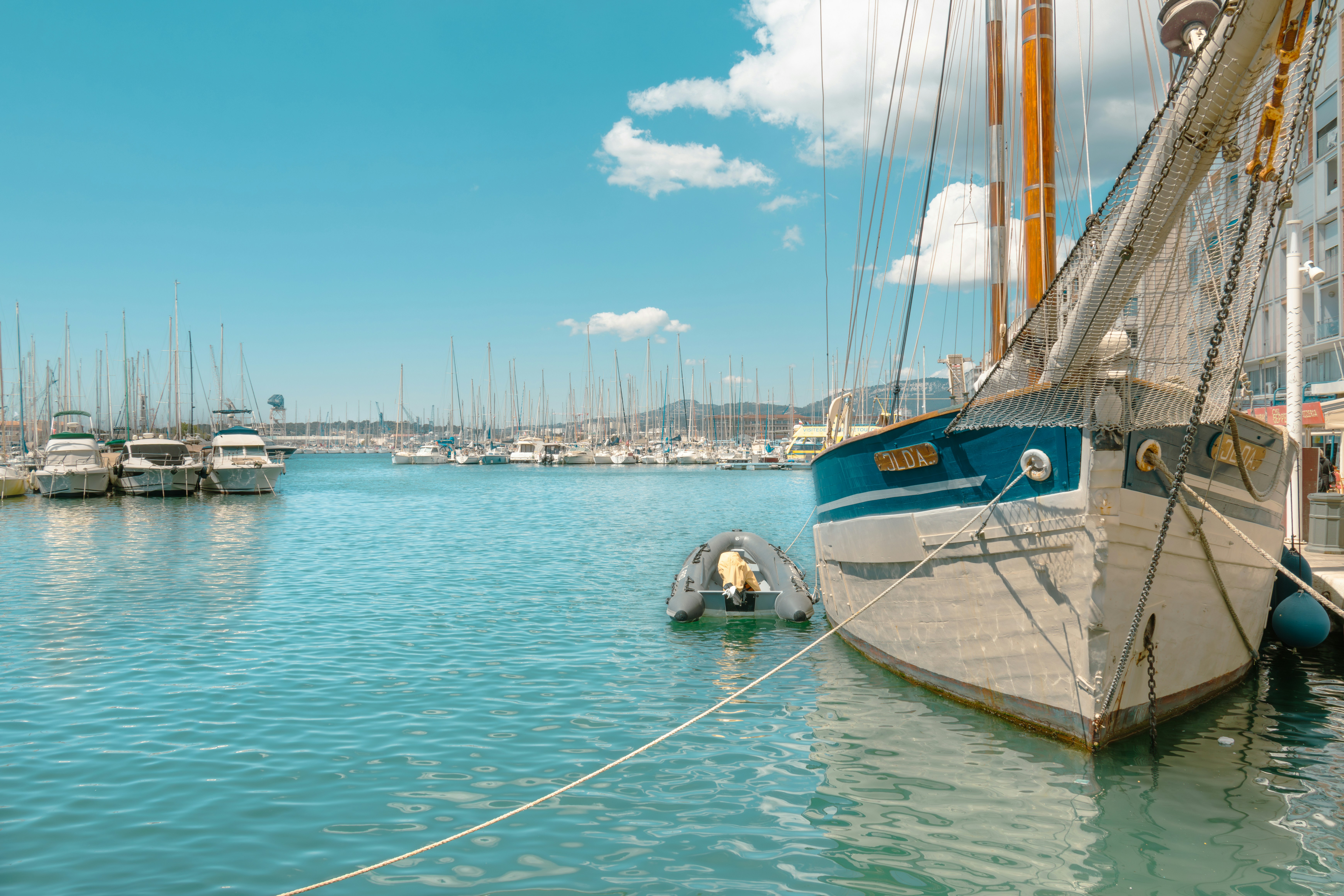 Sailboats anchored in a serene harbor, with a prominent vessel in the foreground reflecting on the turquoise waters.