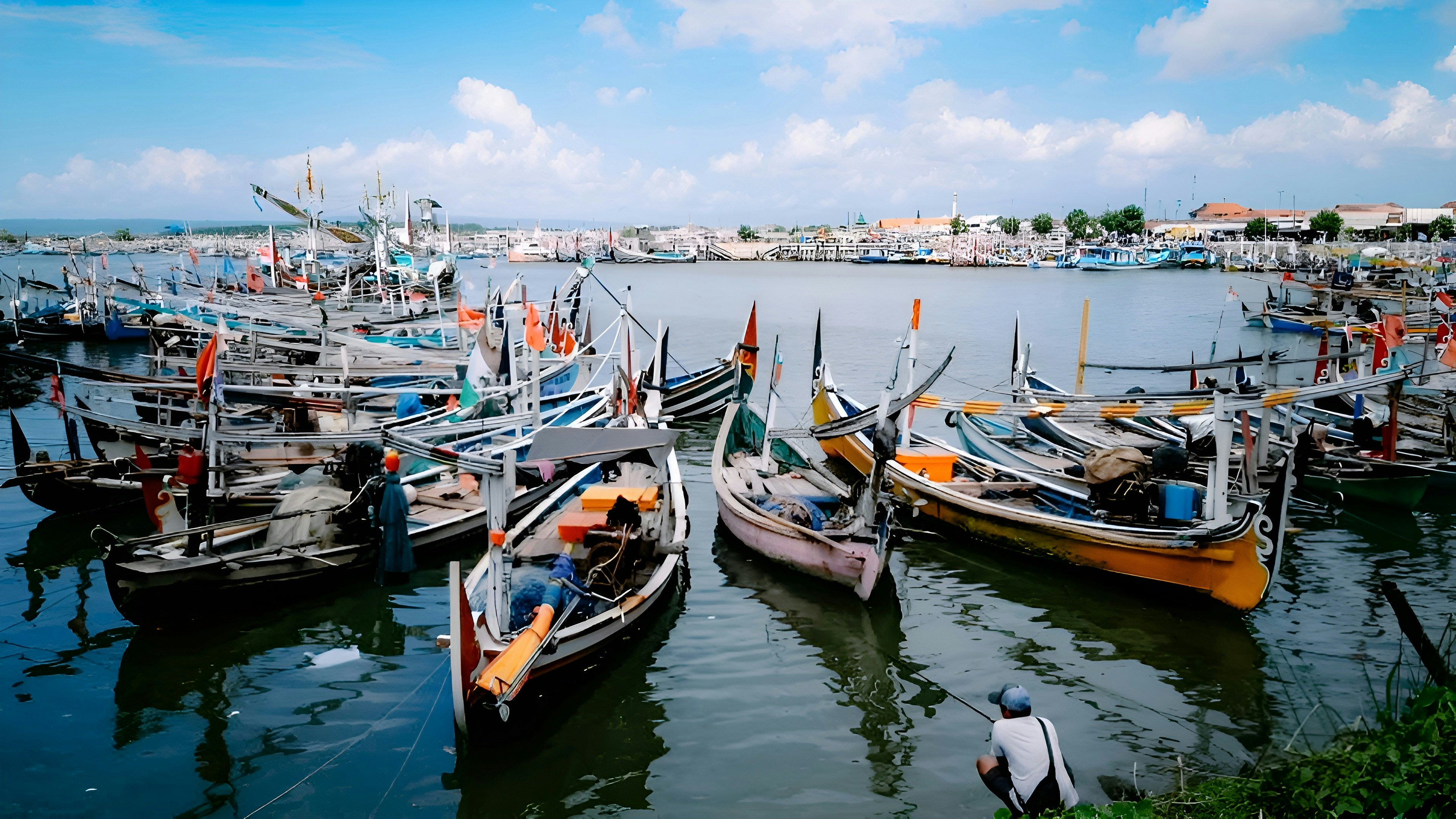 Traditional sailboats with colorful designs moored along the shore of Muncar, Indonesia, under a bright blue sky.