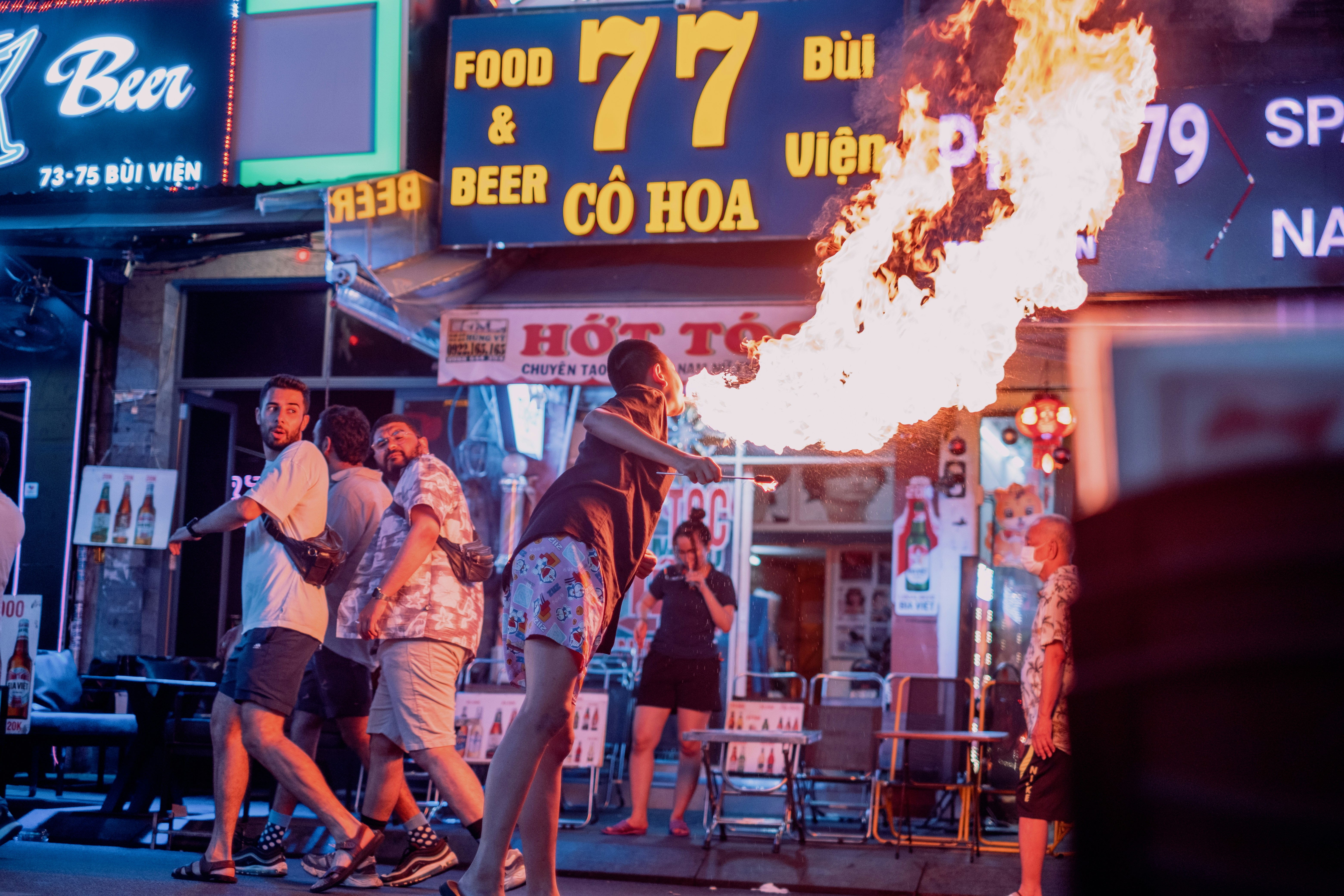 Neon Flame on a Crowded Night Street: Flamethrower Show Under Bright Signage