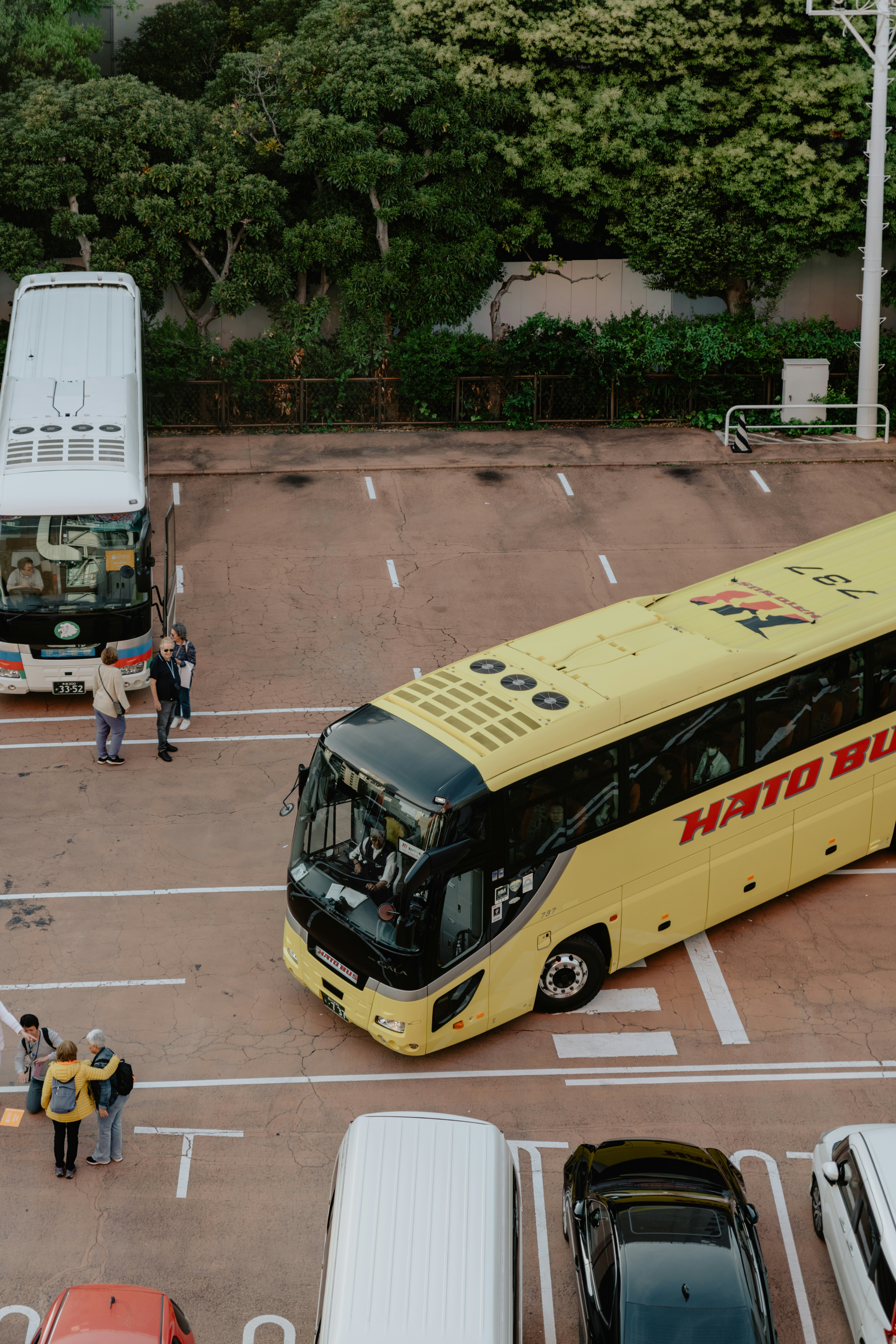 Yellow Bus at Rest: Aerial View of Parking Lot with Tour Buses and Groups