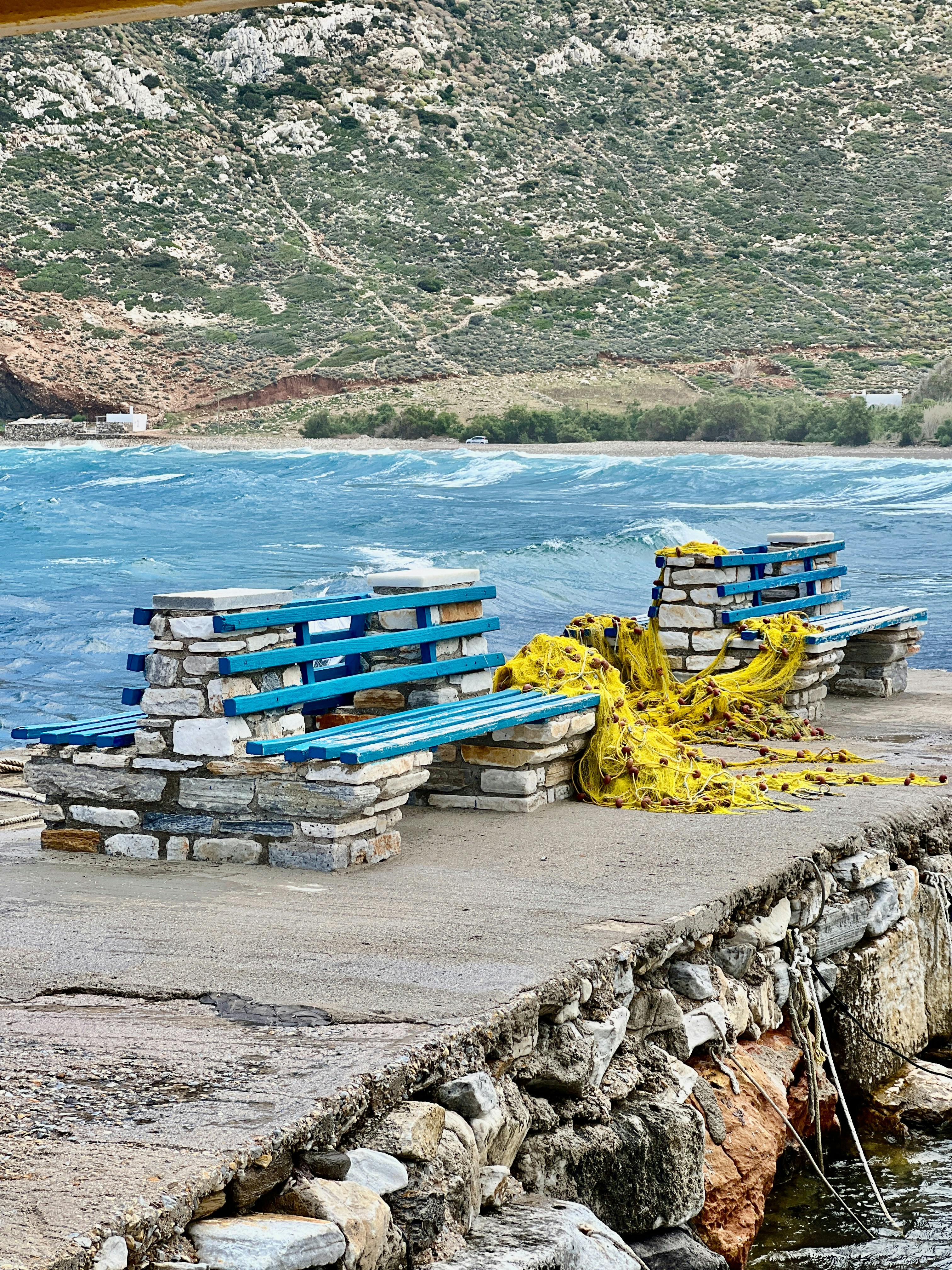 Colorful stone benches adorned with fishing nets line a coastal promenade, overlooking gentle waves lapping at the shore.