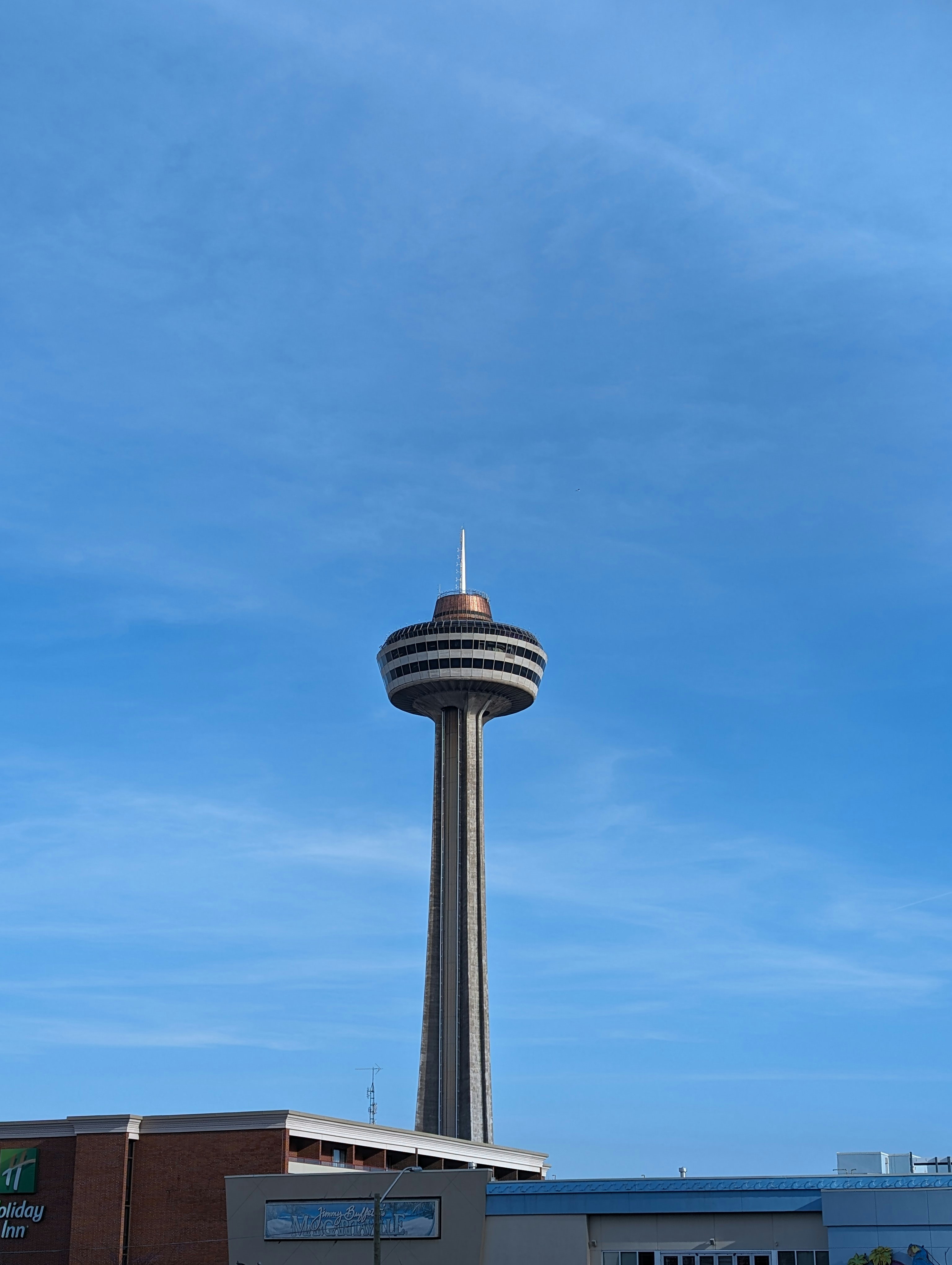 The CN Tower rises above a low-rise urban foreground under a clear blue sky.