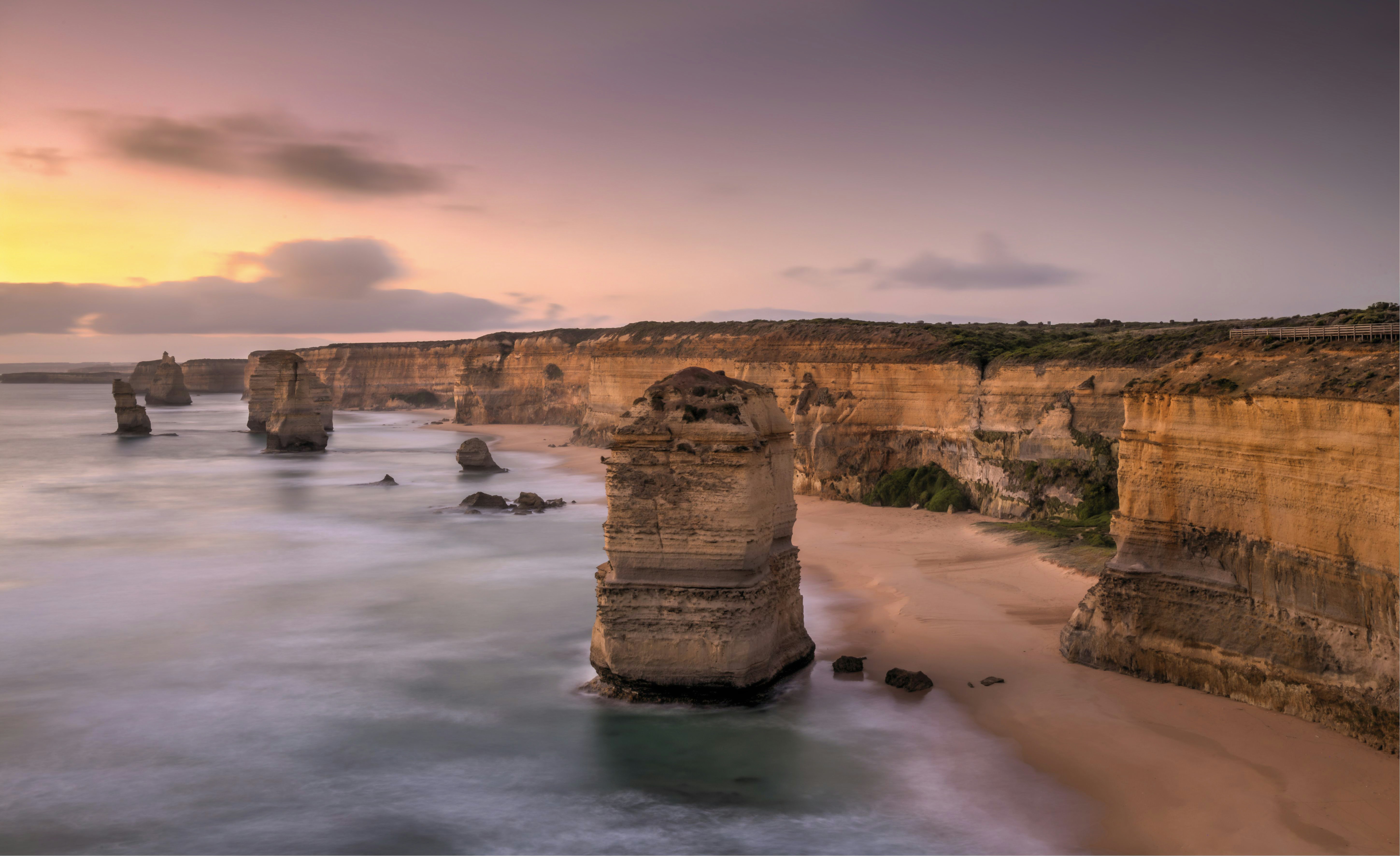 Majestic limestone stacks rise from the shore, surrounded by gentle waves and golden sands at twilight.