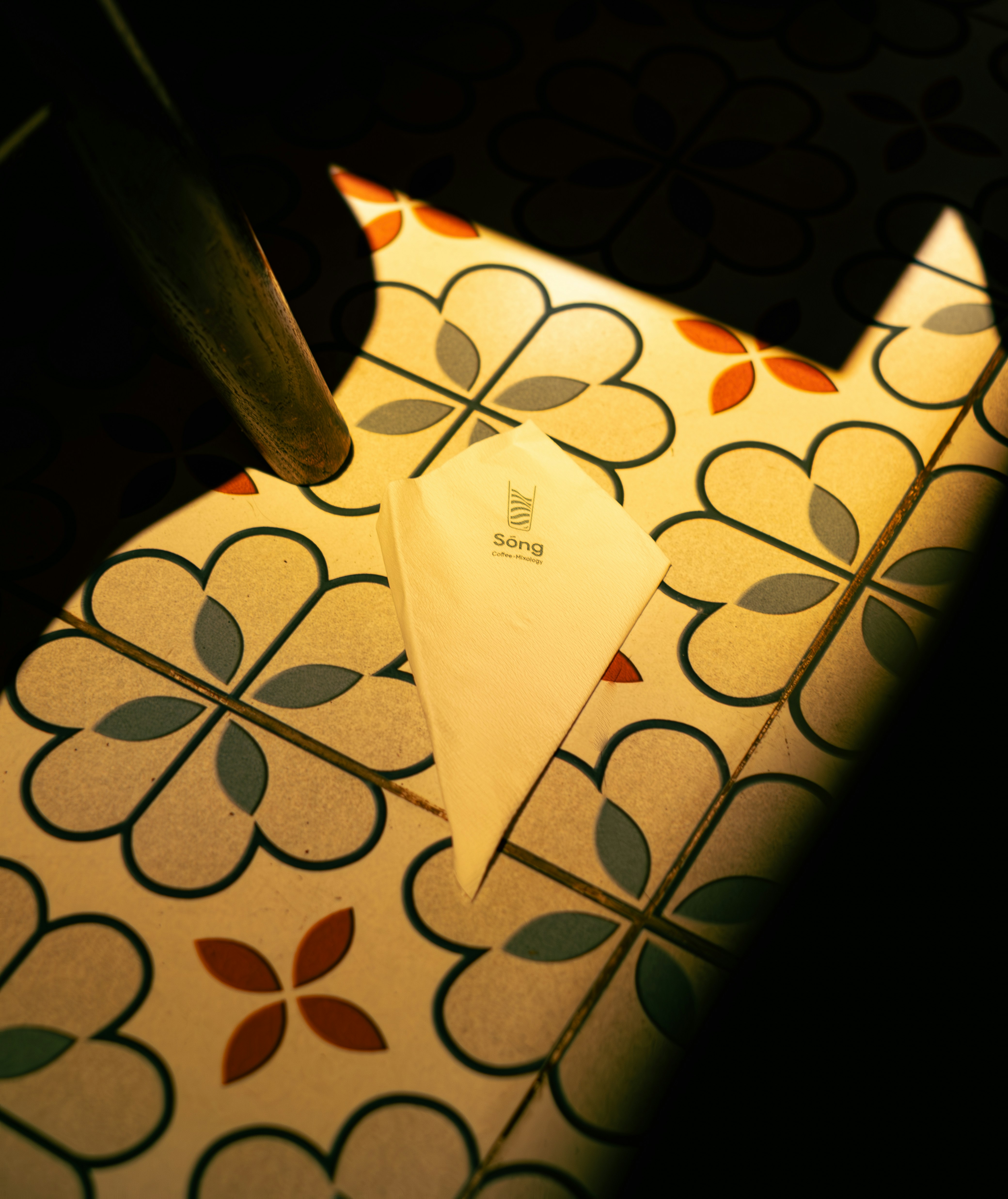 Amber Spotlight on a Folded Napkin with Song Logo on a Mosaic Floor