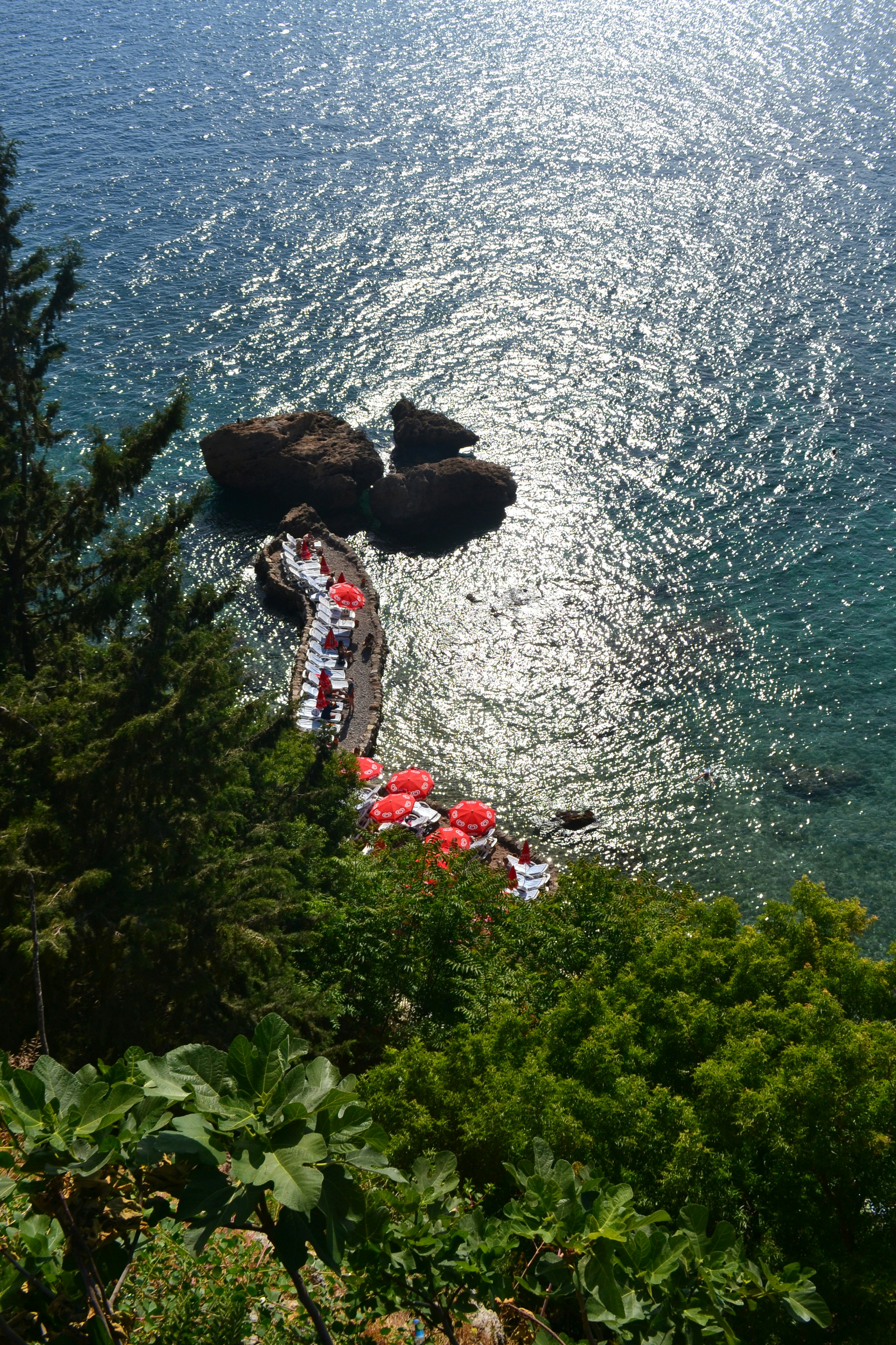 Sunlit Turquoise Cove: Red Parasols on a Narrow Jetty