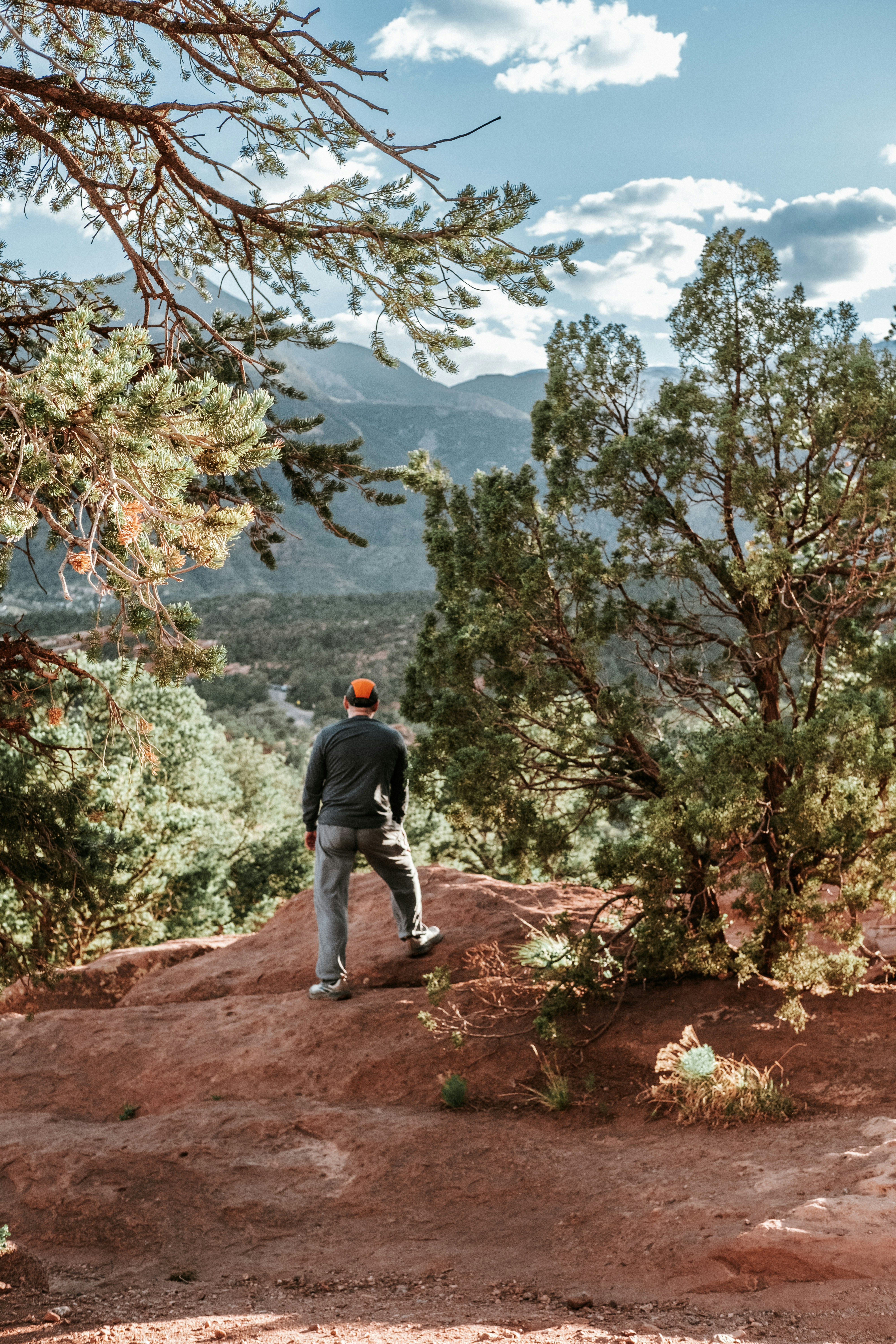 Cliffside Gazer: A man in a bright cap surveys a canyon from a red rock ledge