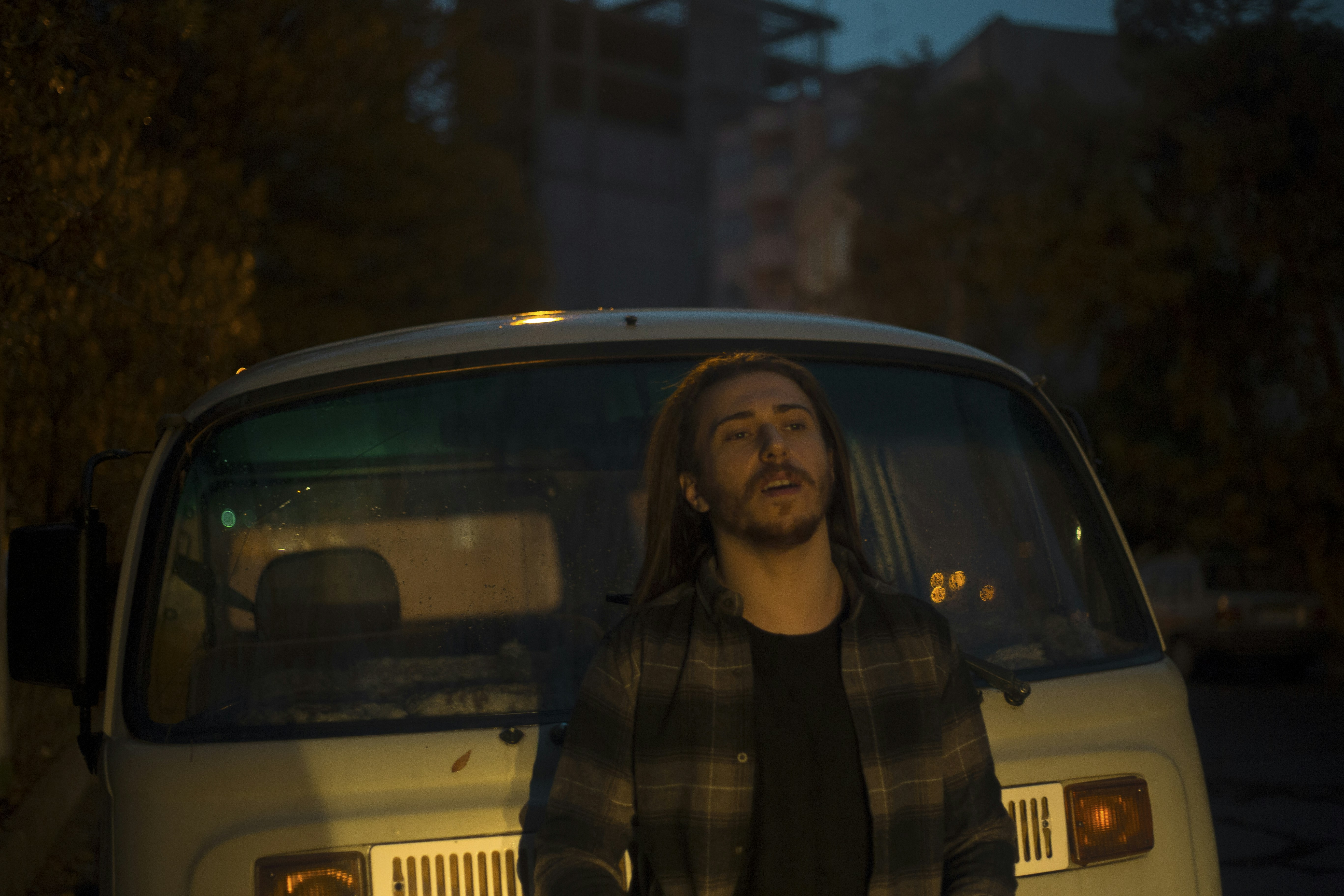 Person standing in front of an old van at dusk with blurred urban background.
