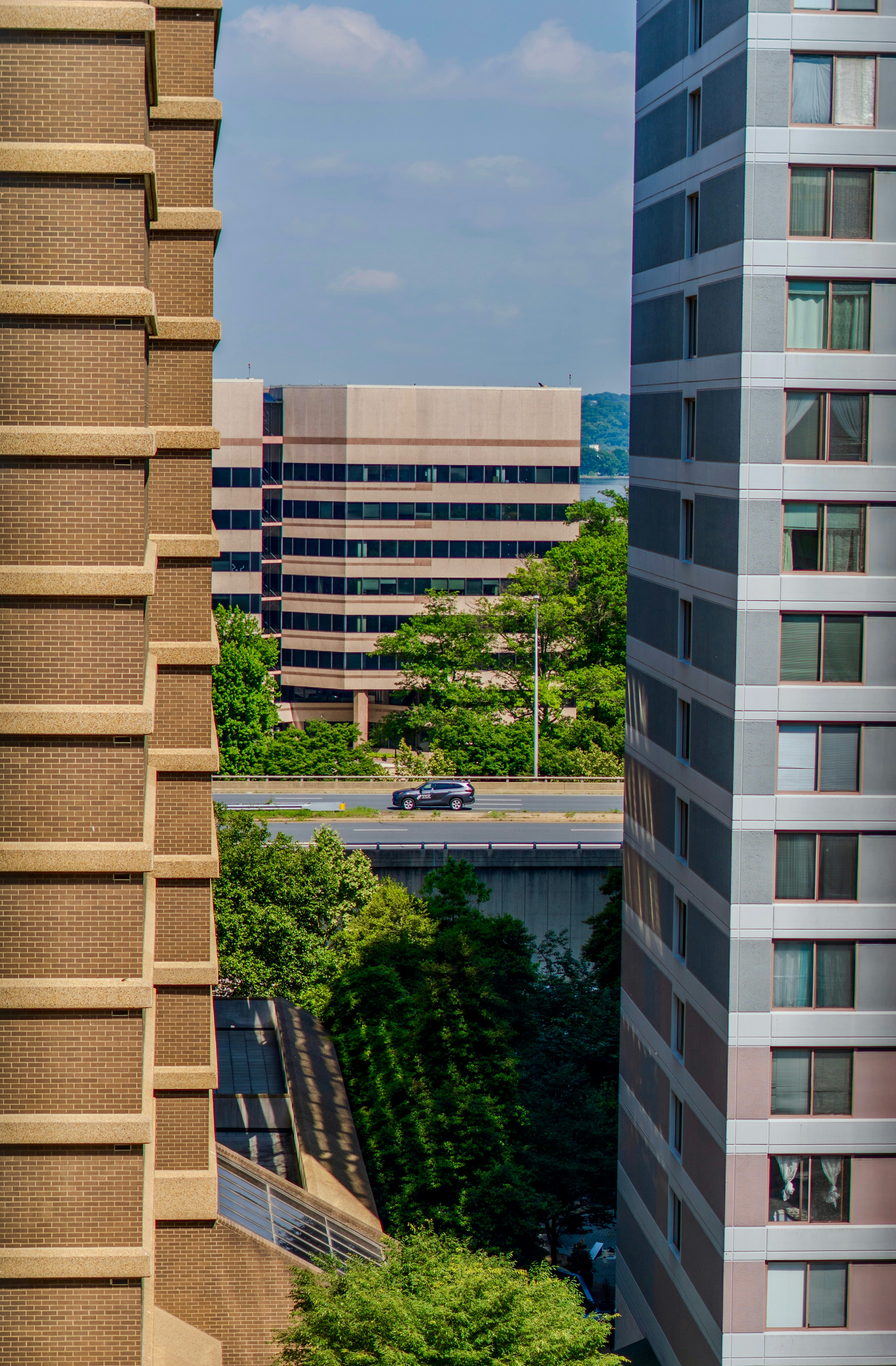 A view of a cityscape framed by two tall buildings, showcasing a glimpse of the road and greenery beyond. The scene captures the intersection of architecture and nature.