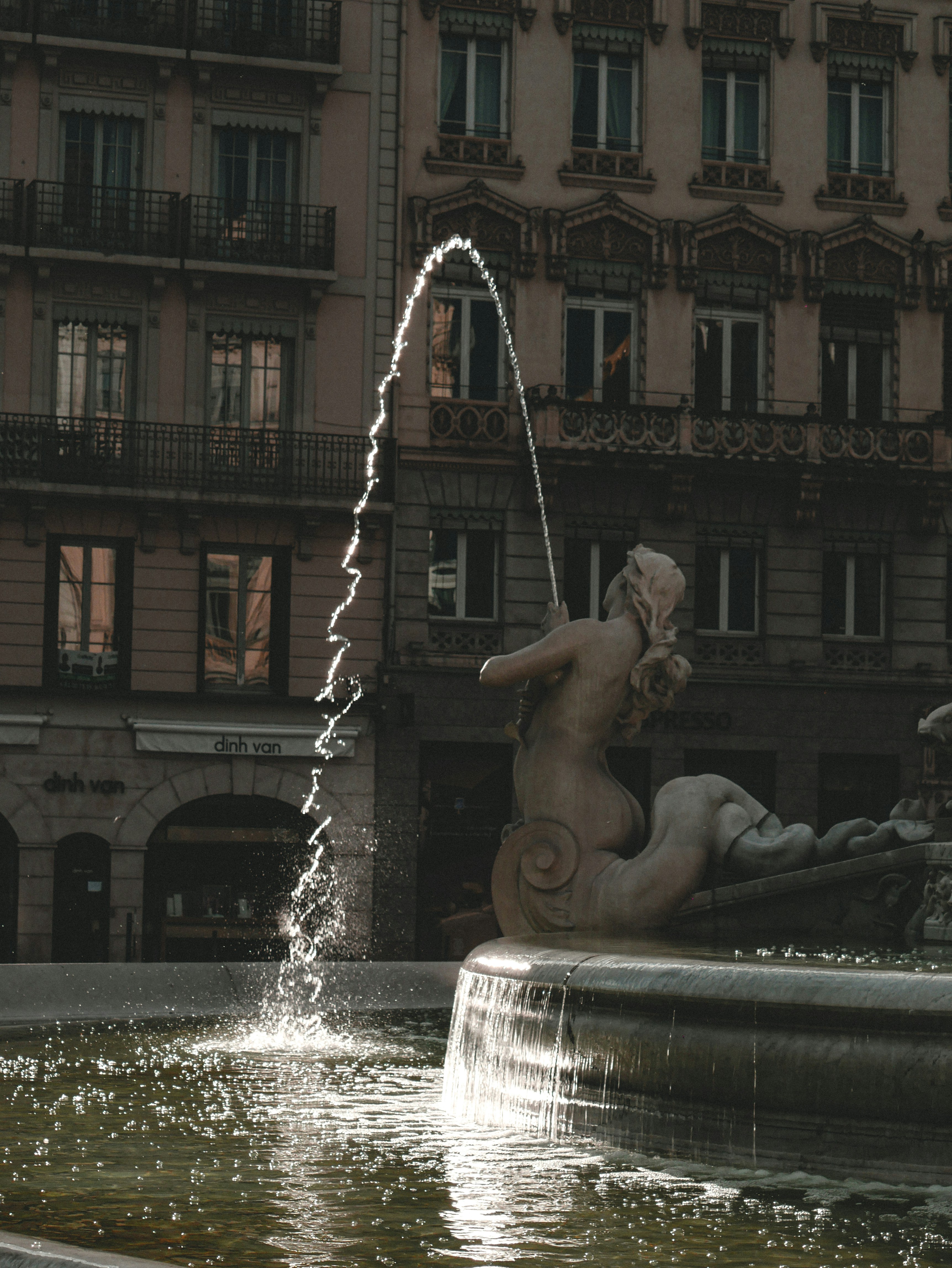 A fountain with water shooting out of it in front of a building photo ...