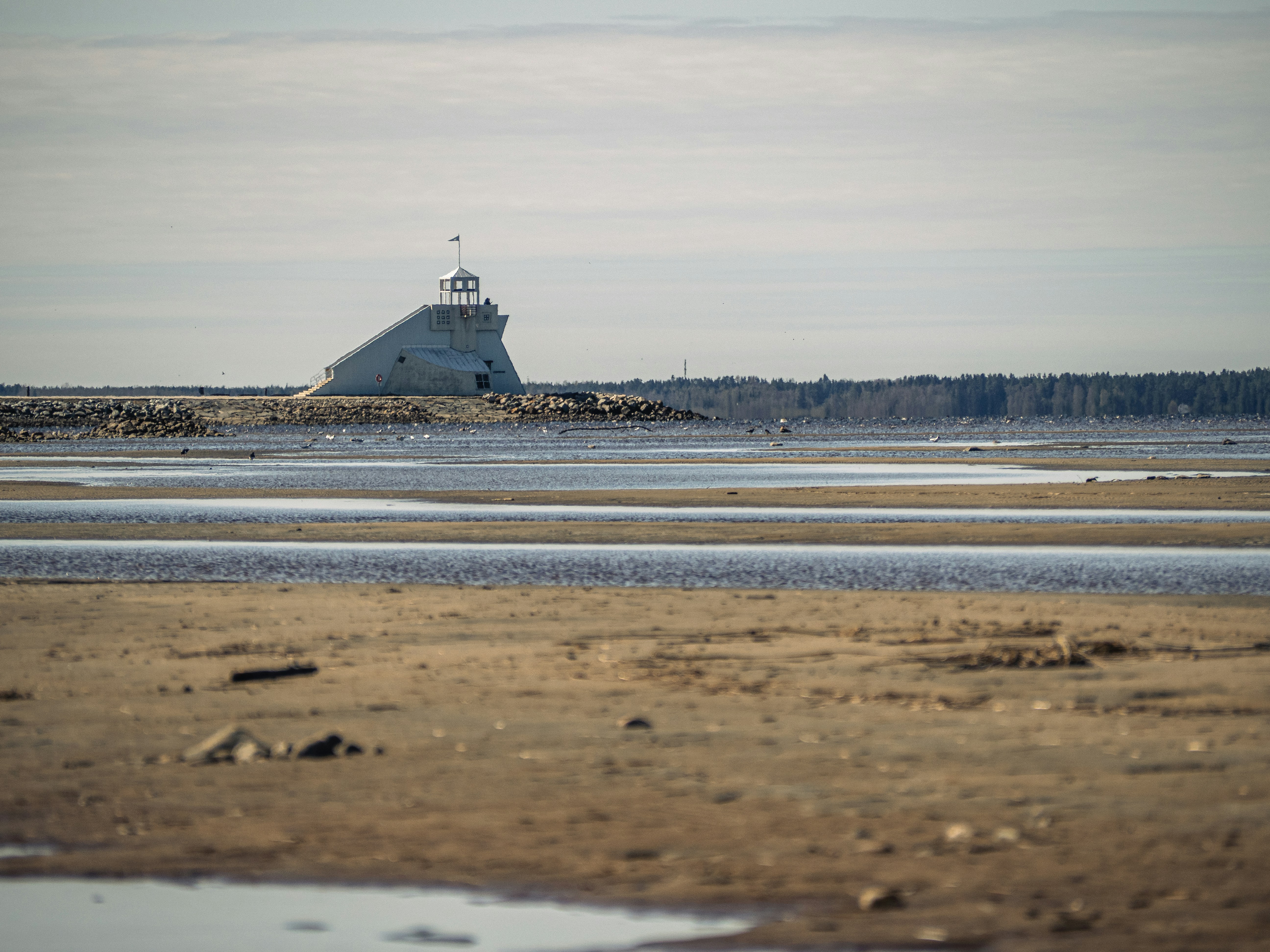 Lighthouse perched on a distant island surrounded by calm water and expansive sky.