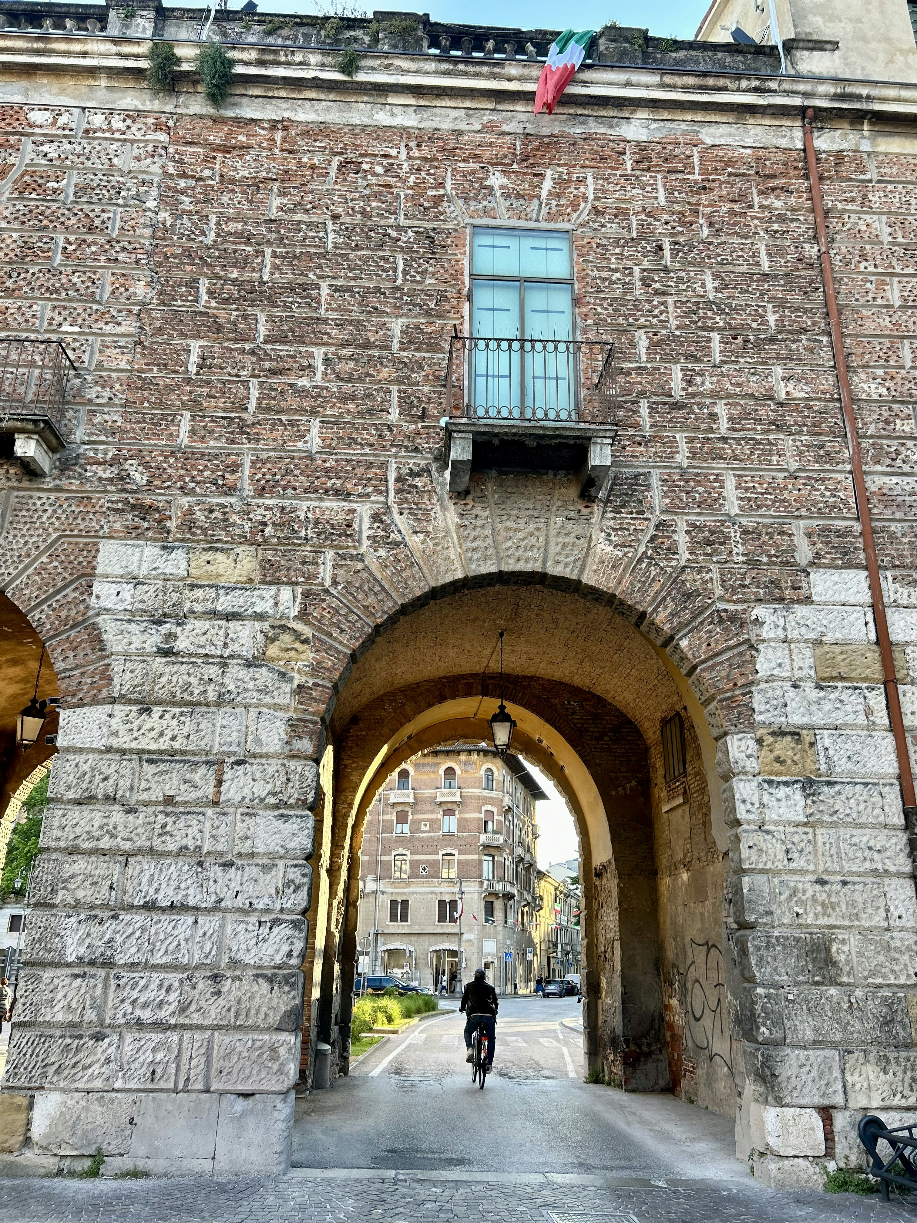 Under the Stone Arch: A Cyclist Navigates an Italian Gateway Framed by Weathered Brick