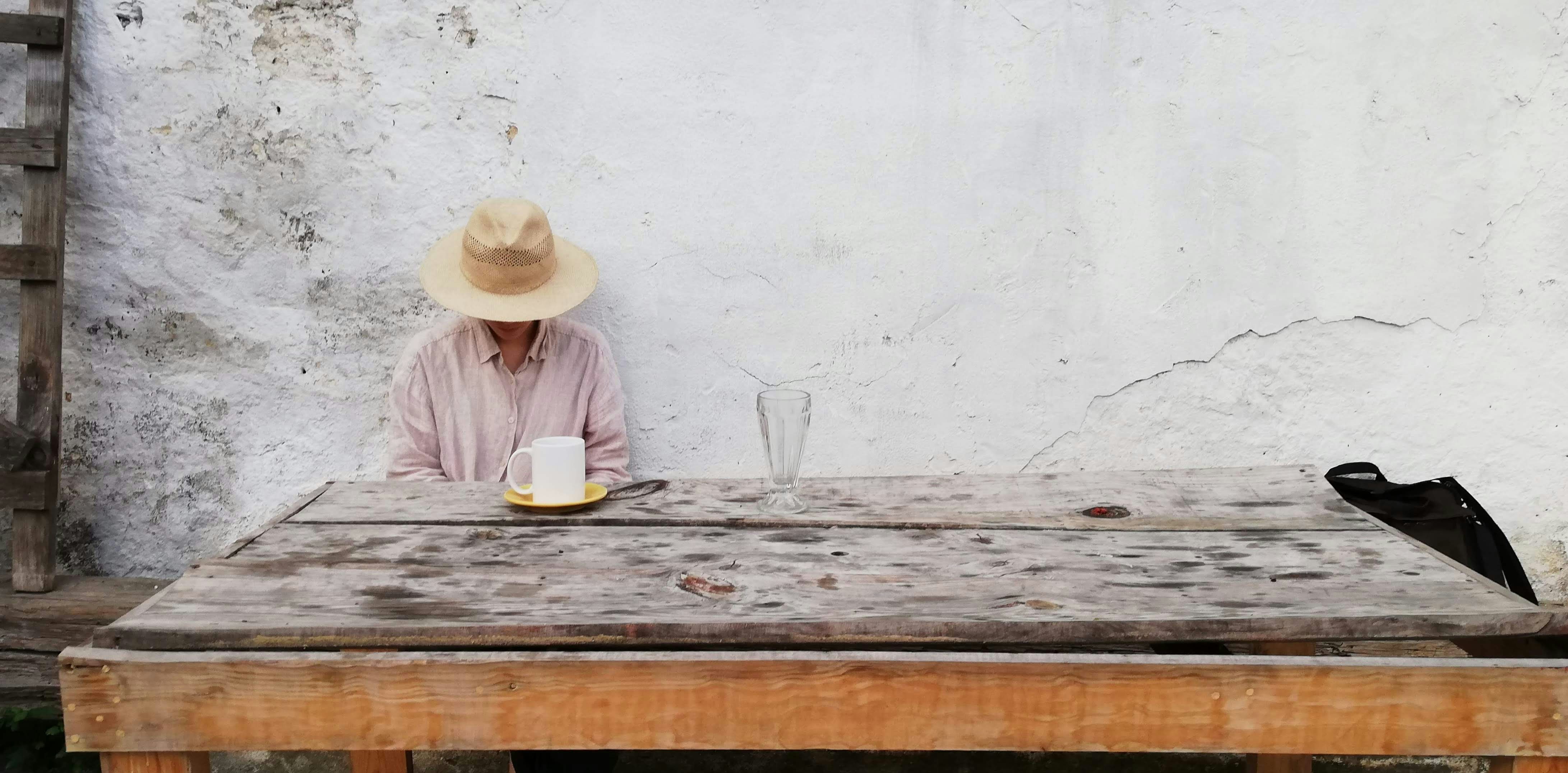 Person in a straw hat sitting at a rustic wooden table against a textured wall.
