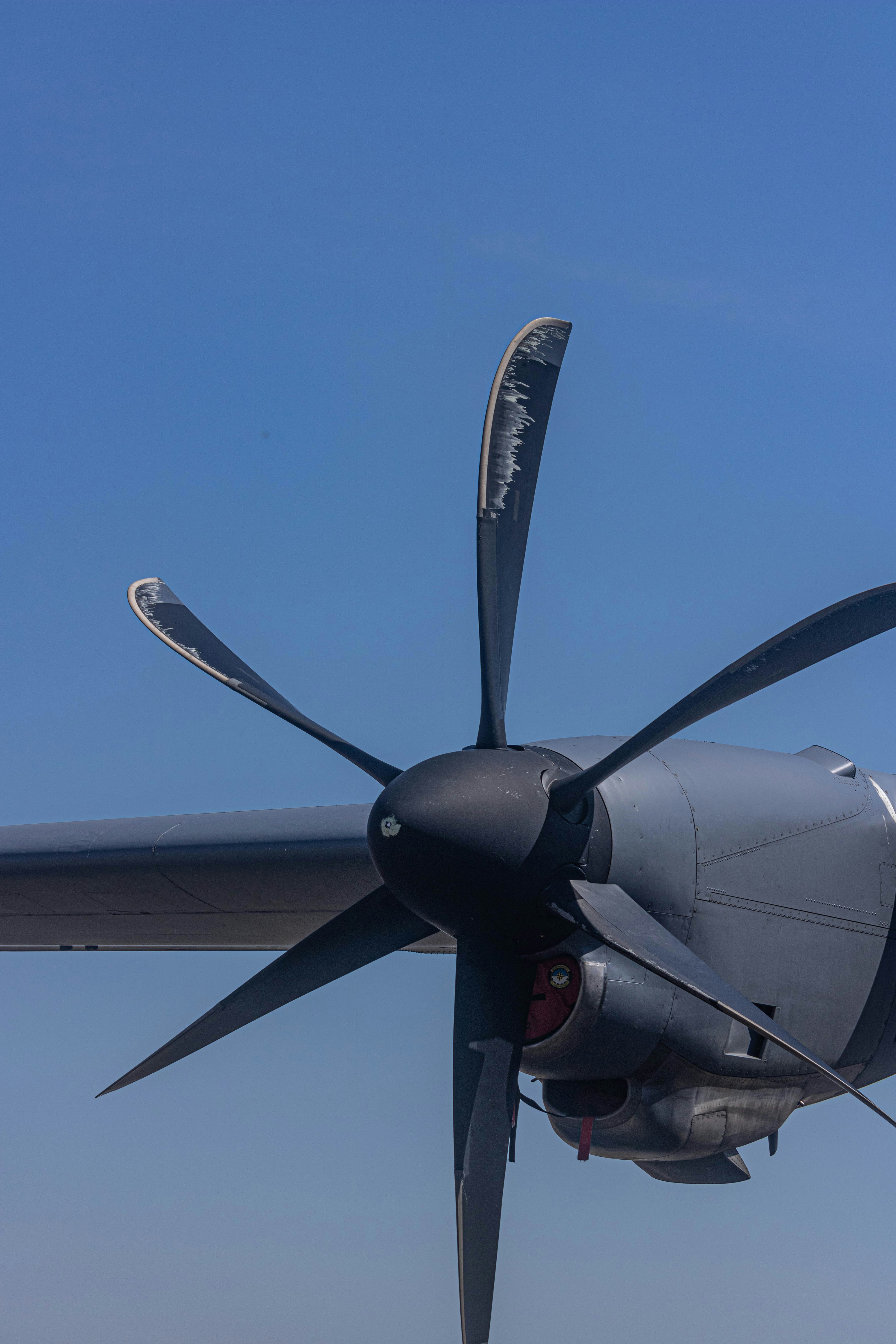 Close-up photograph of a turboprop engine hub with four blades set against a clear blue sky.