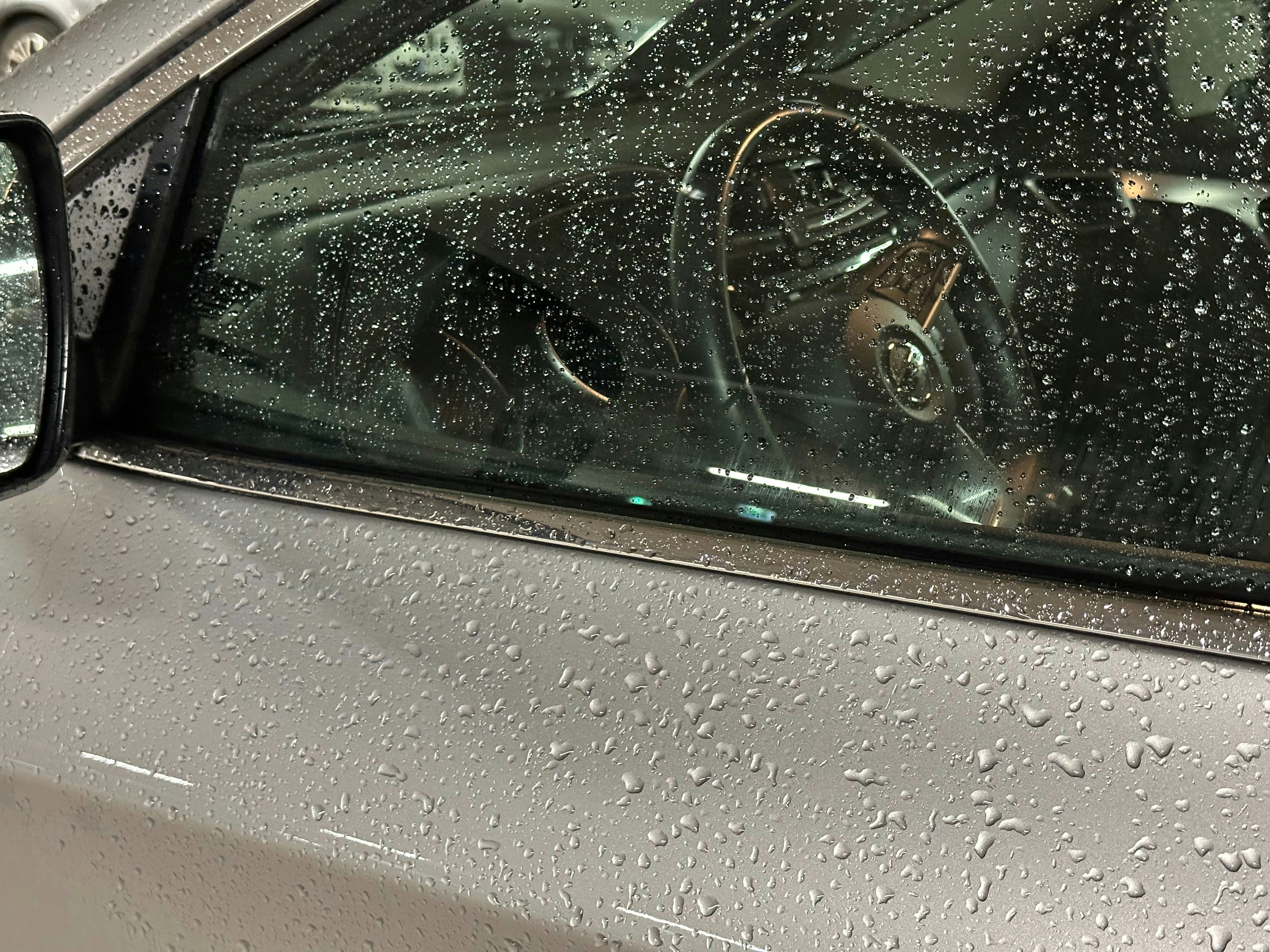 Rain-Glossed Window Frames a Quiet Interior: Steering Wheel Under Droplets