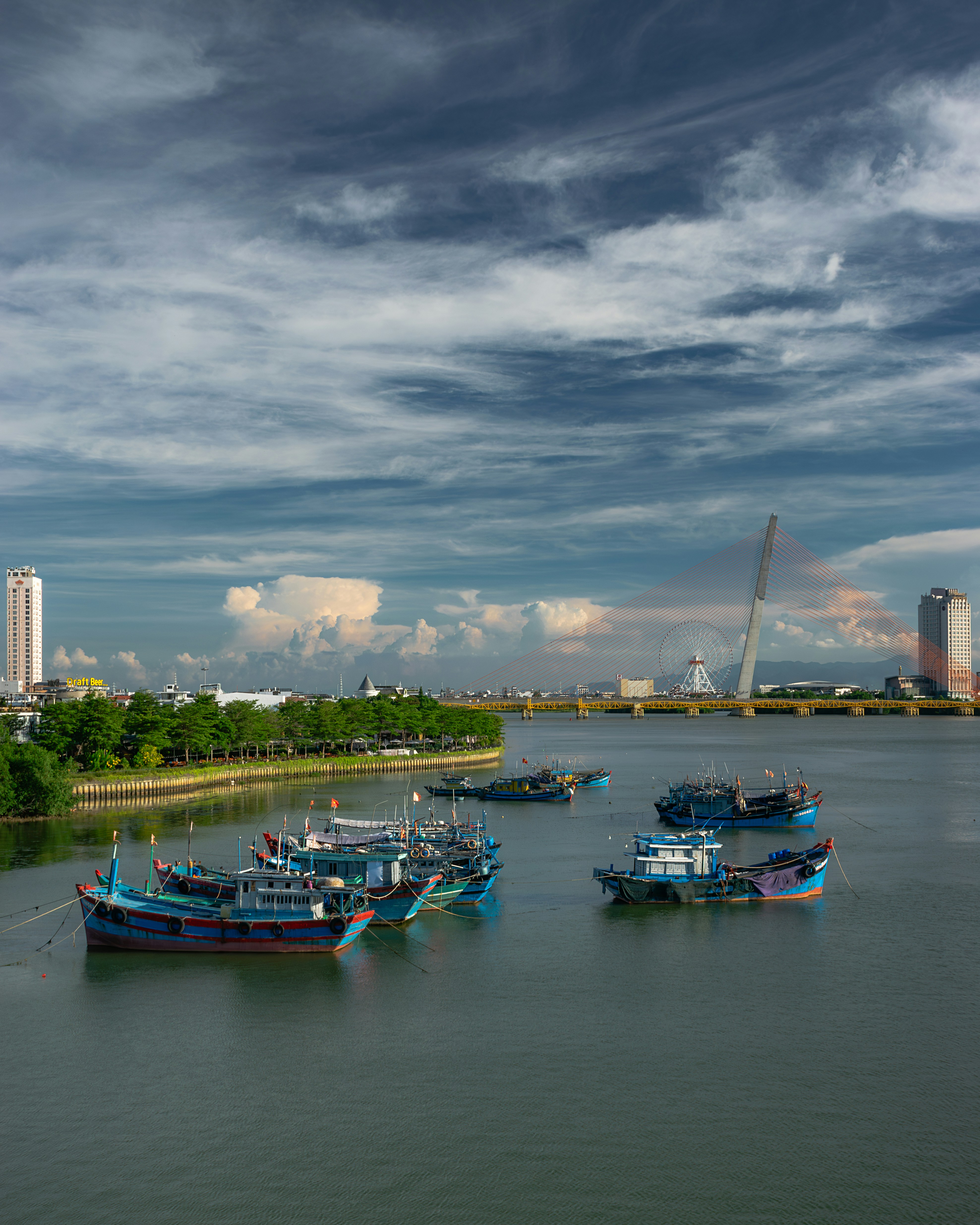 Fishing boats anchored in a serene river, framed by modern skyscrapers and dramatic clouds. The scene captures the blend of nature and urban life.