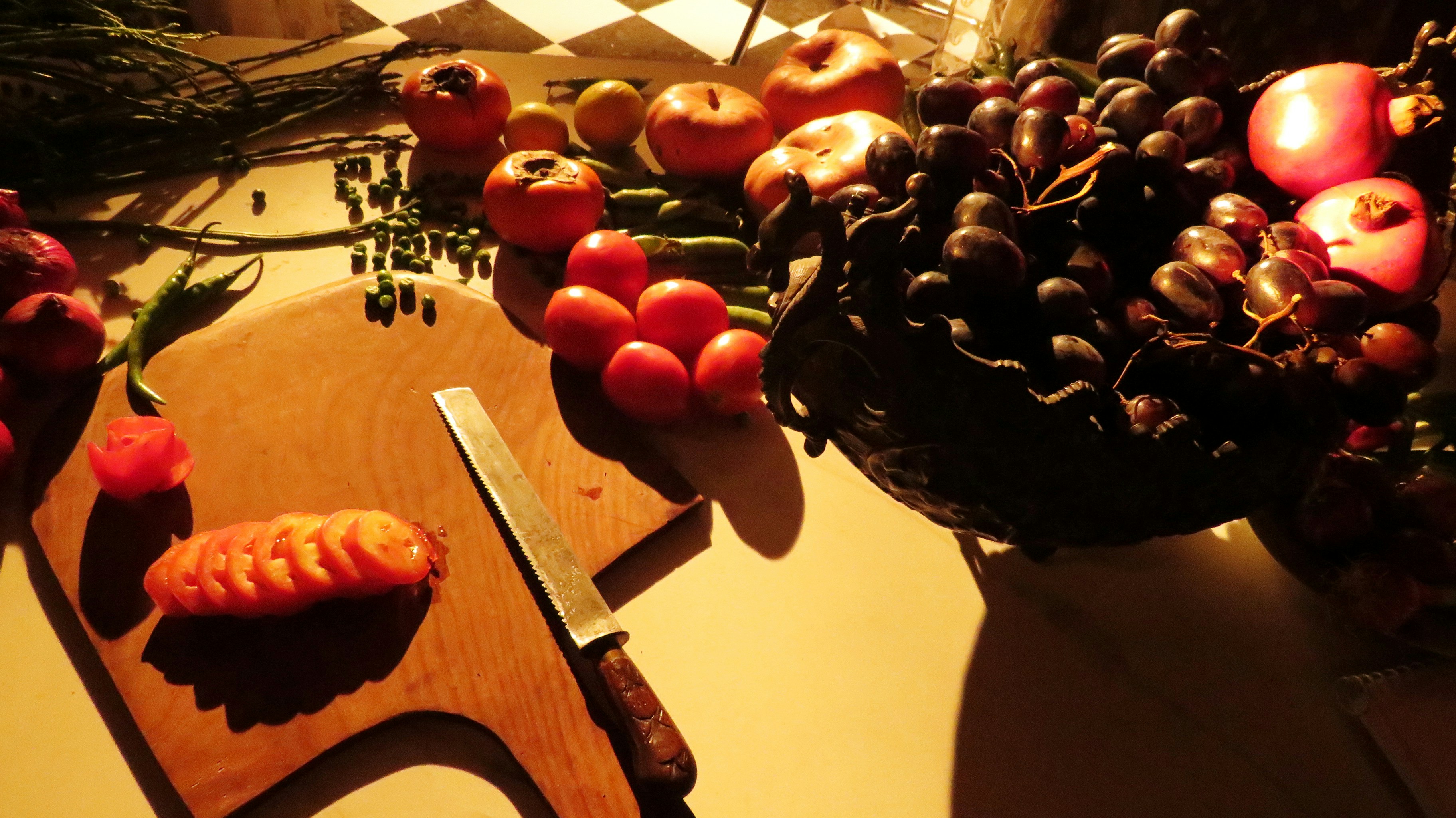 Twilight Kitchen Still Life: Carrot Slice on Wood Cutting Board Beside a Basket of Grapes
