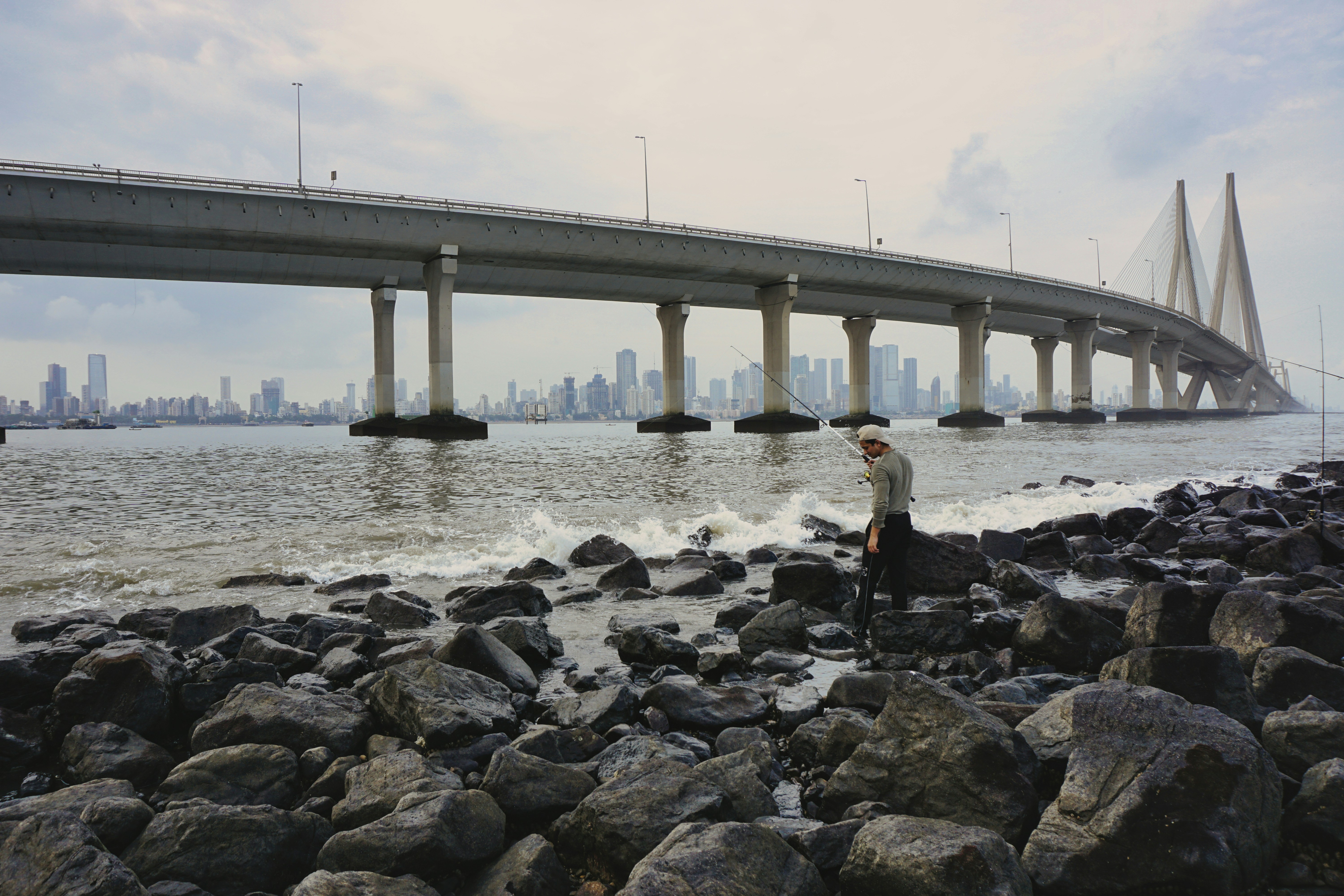 Edge of the Tide: A lone figure anchors the jagged shoreline beneath a sweeping bridge