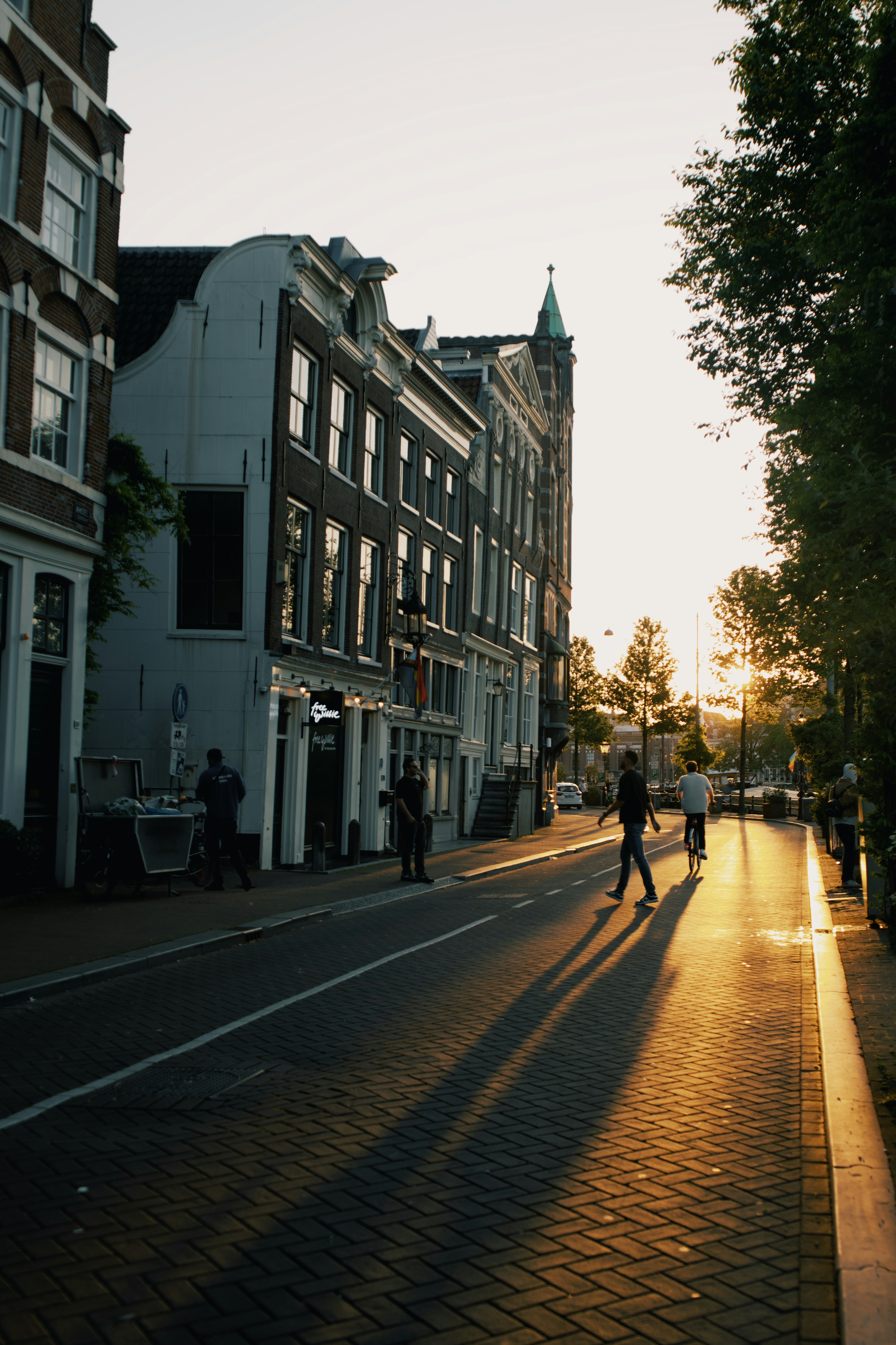 Warm sunlight casts long shadows on a cobblestone street lined with historic buildings, capturing the essence of a tranquil evening in a vibrant city.
