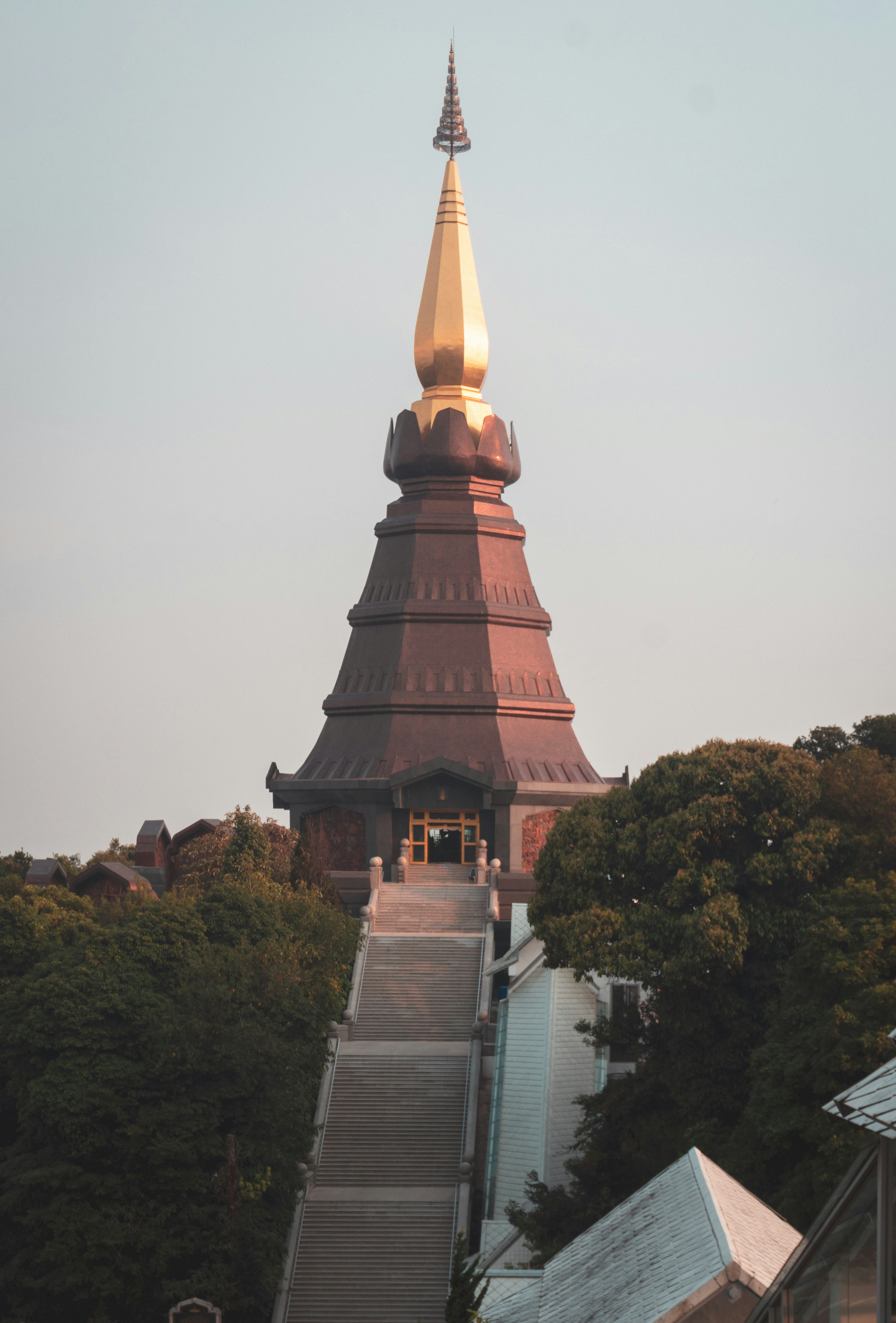 Towering temple structure with a golden spire, surrounded by lush greenery and pathways leading up to it.
