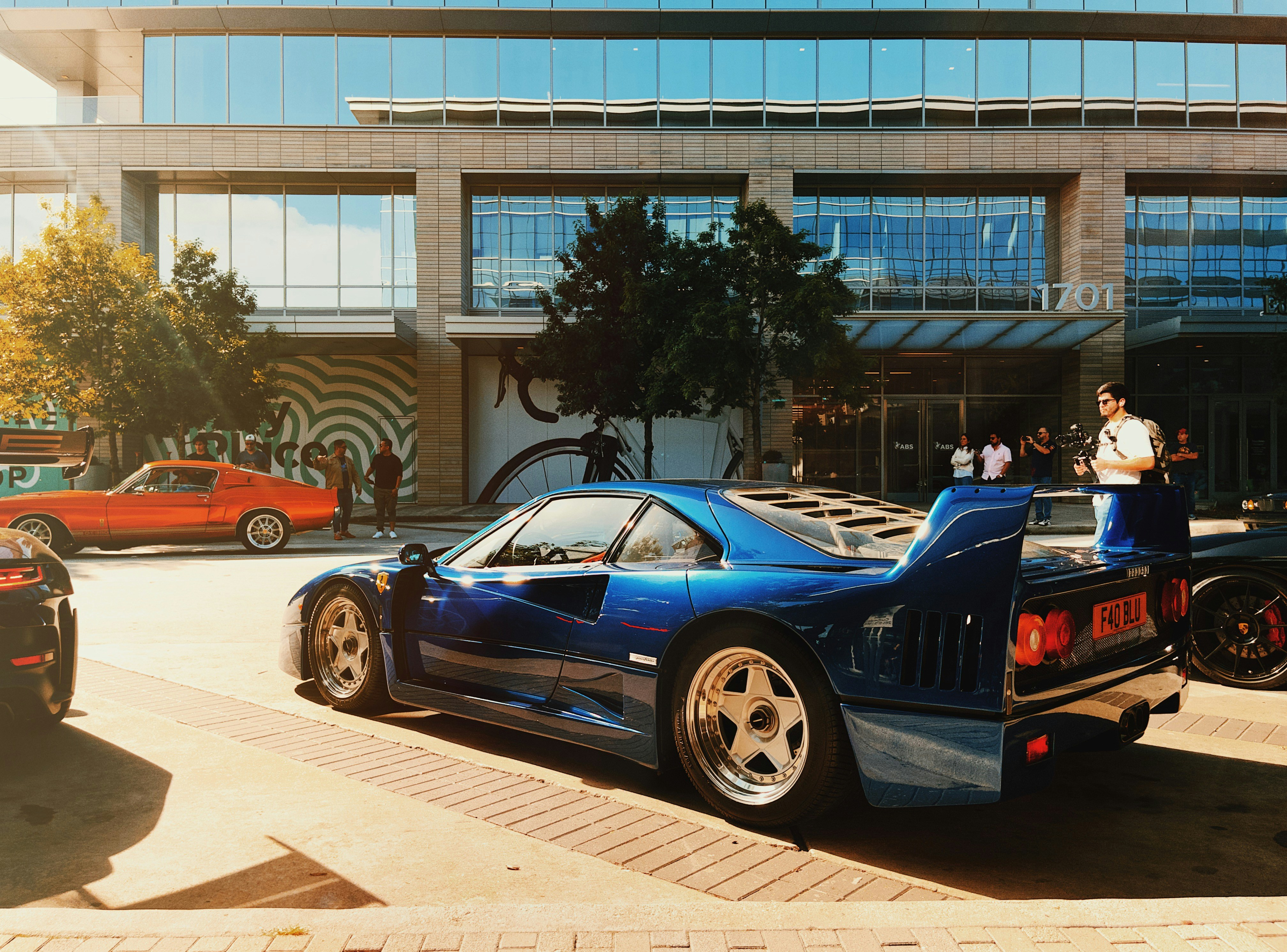 Blue sports car parked in front of a modern glass building under the afternoon sun.