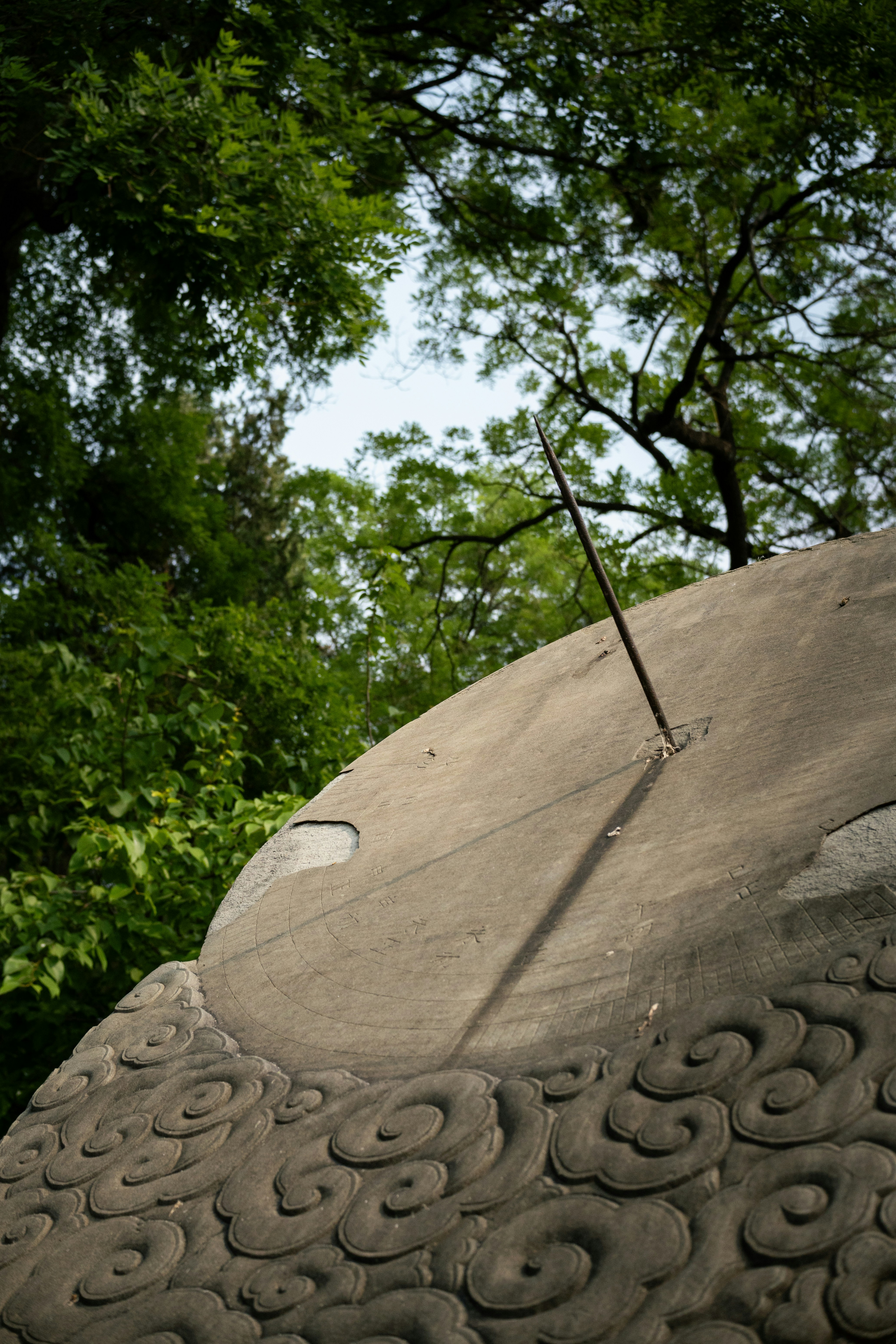 Intricately carved sundial nestled among lush greenery, showcasing a metal gnomon casting shadows on its surface.
