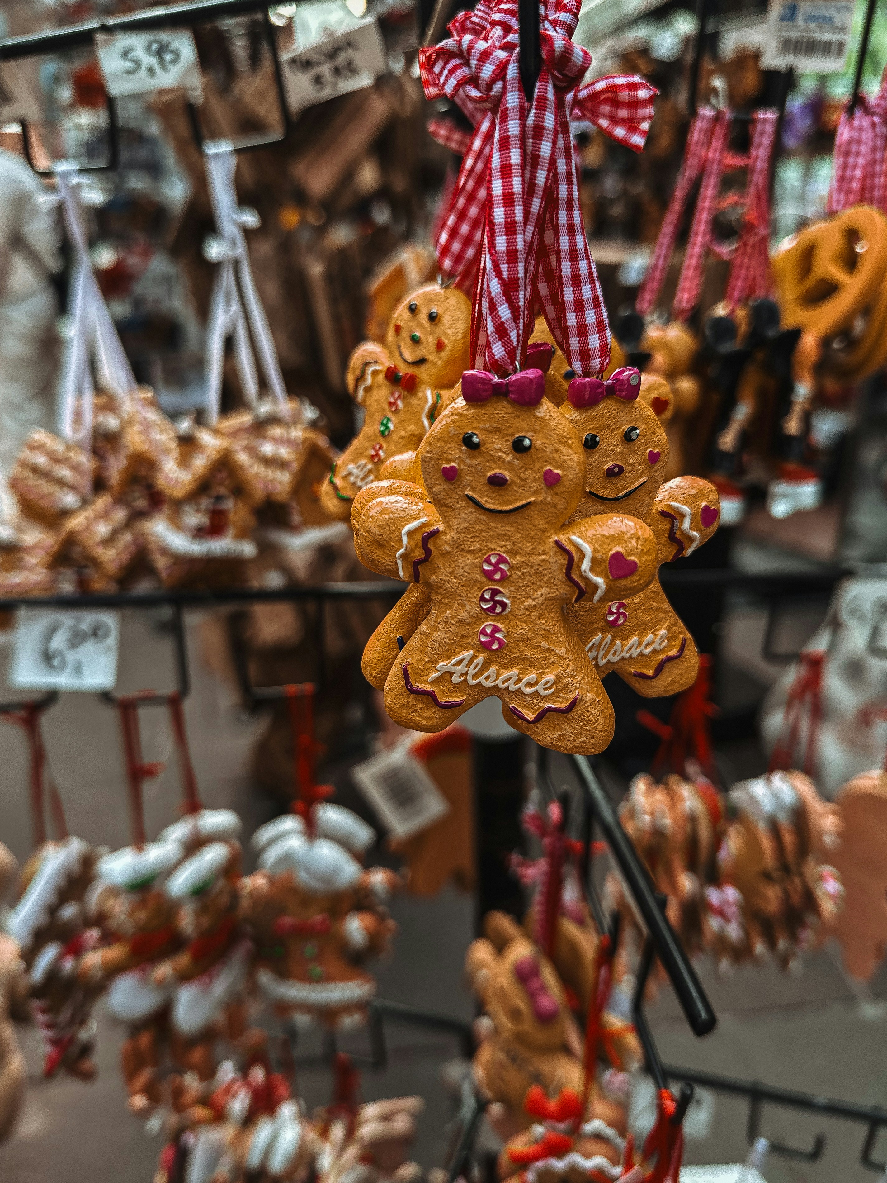Close-up of festive gingerbread ornaments hanging in a bustling market, with a central cookie inscribed 'Alsace' and smiling faces.
