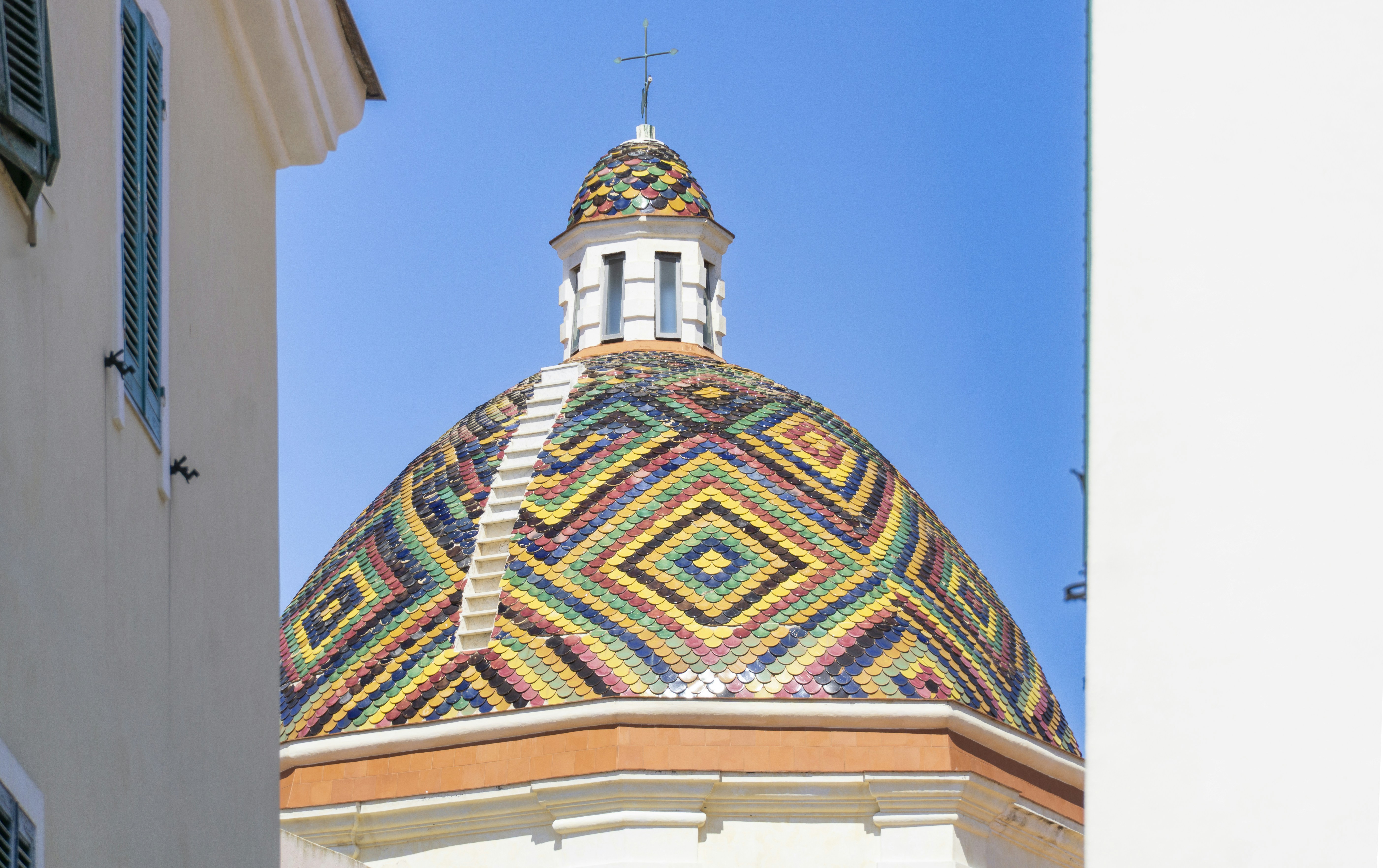 Colorful patterned dome of a building framed by two white walls under a clear blue sky.