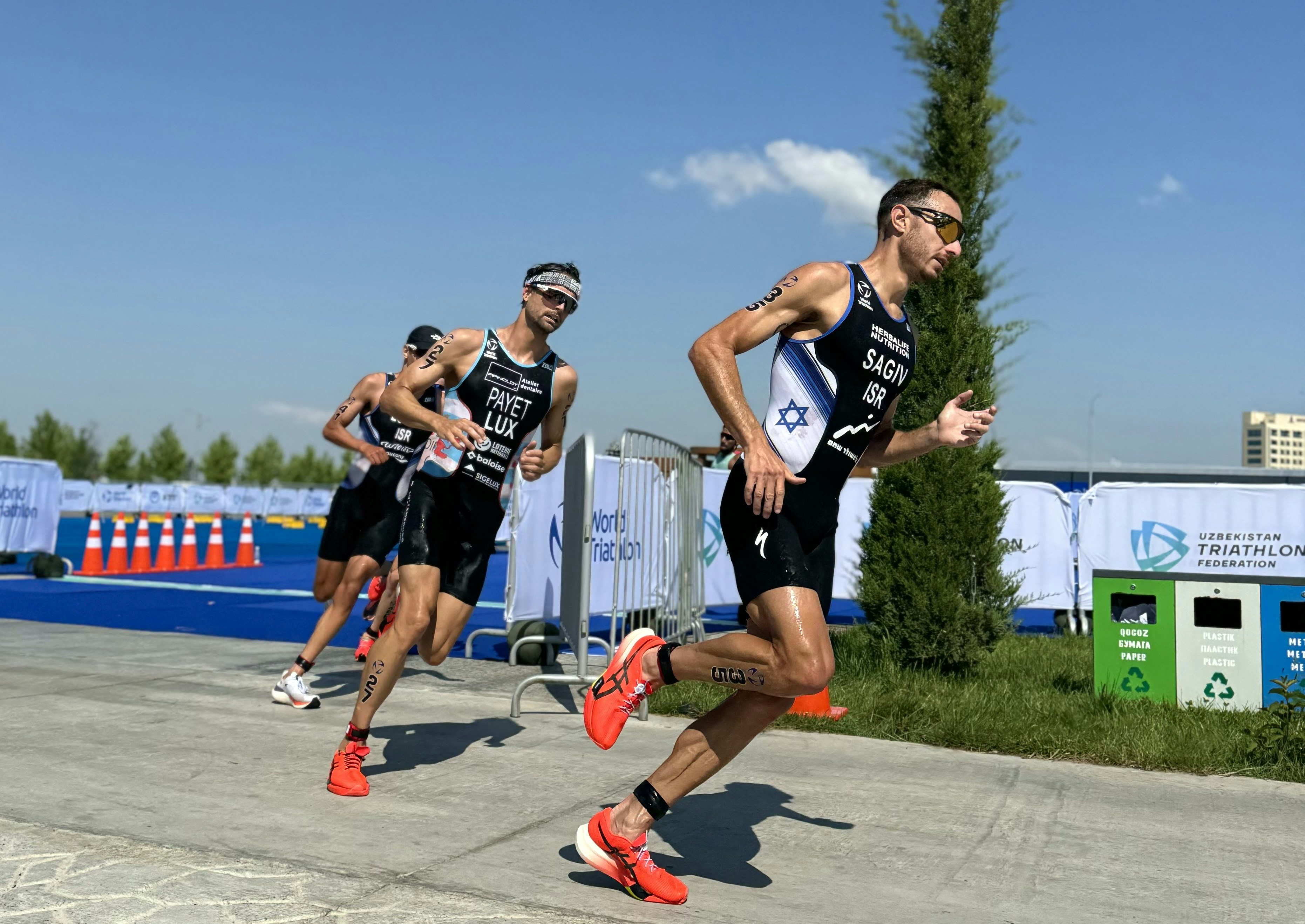 Triathletes sprint along a sunlit path during the World Triathlon Cup in Samarkand, showcasing athletic endurance.