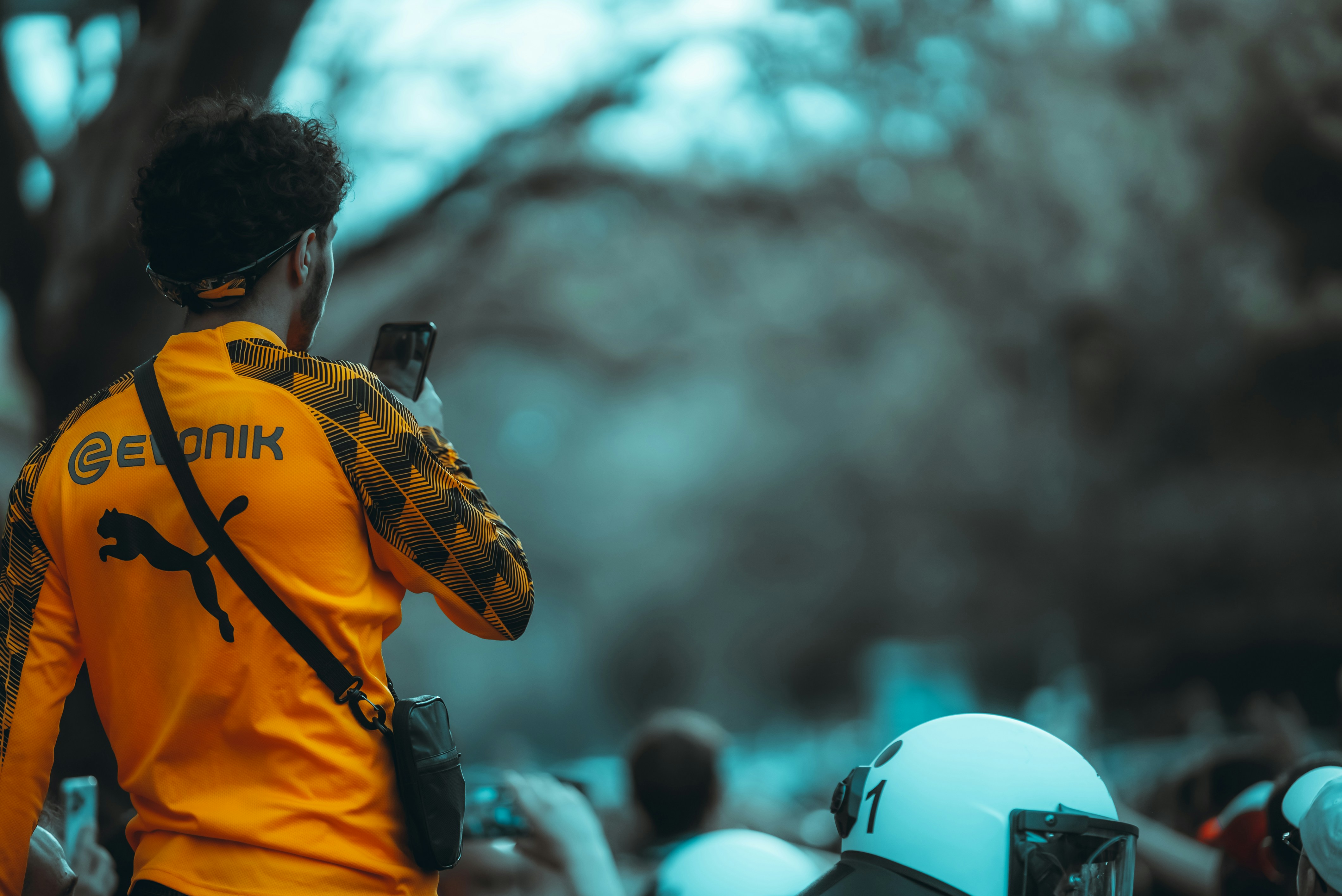 Orange-Jacket Moment: A lone photographer frames a crowd beneath a cyan canopy