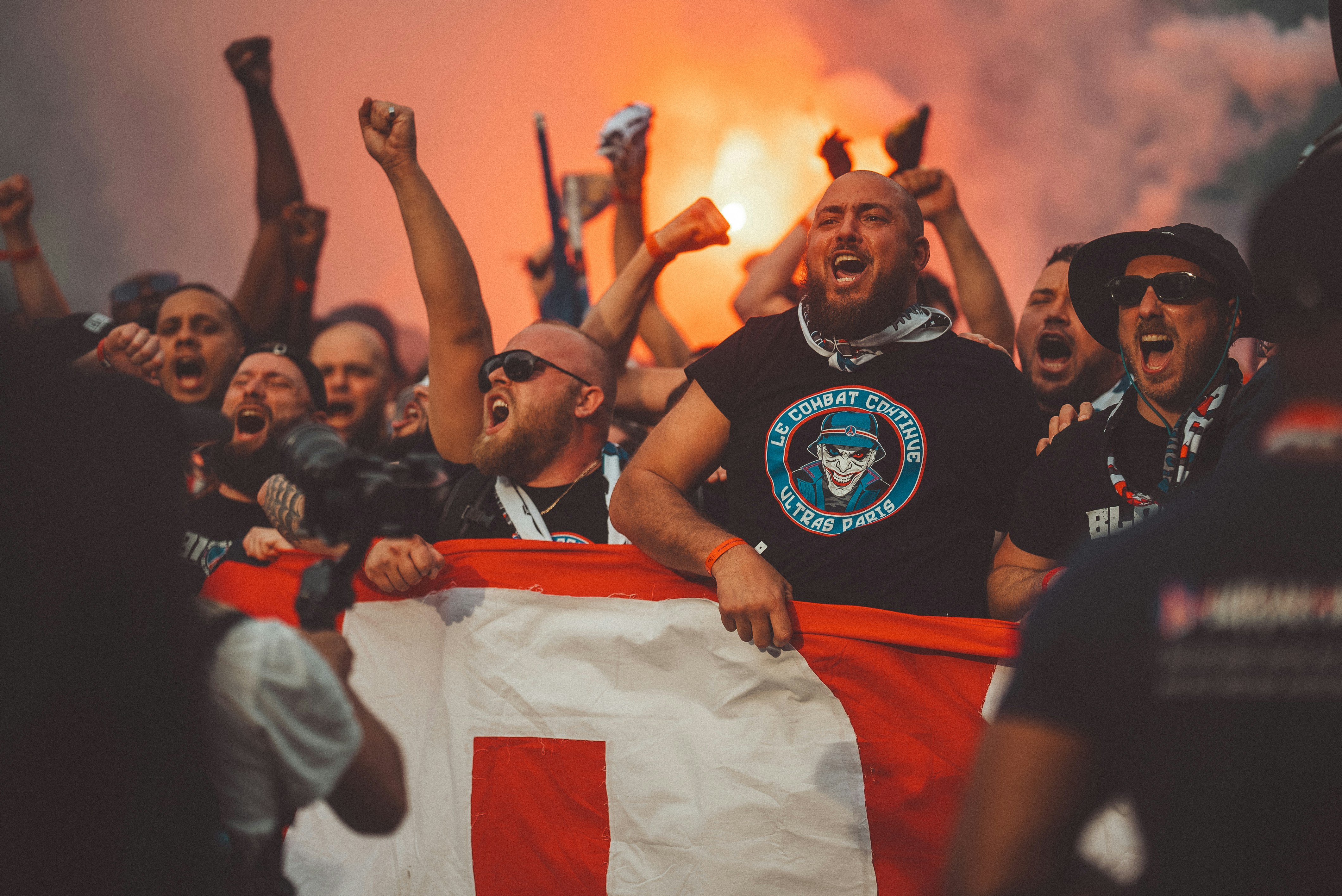 A passionate crowd rallies together, waving a flag and expressing fervor during a vibrant event. The atmosphere is charged with excitement and camaraderie.