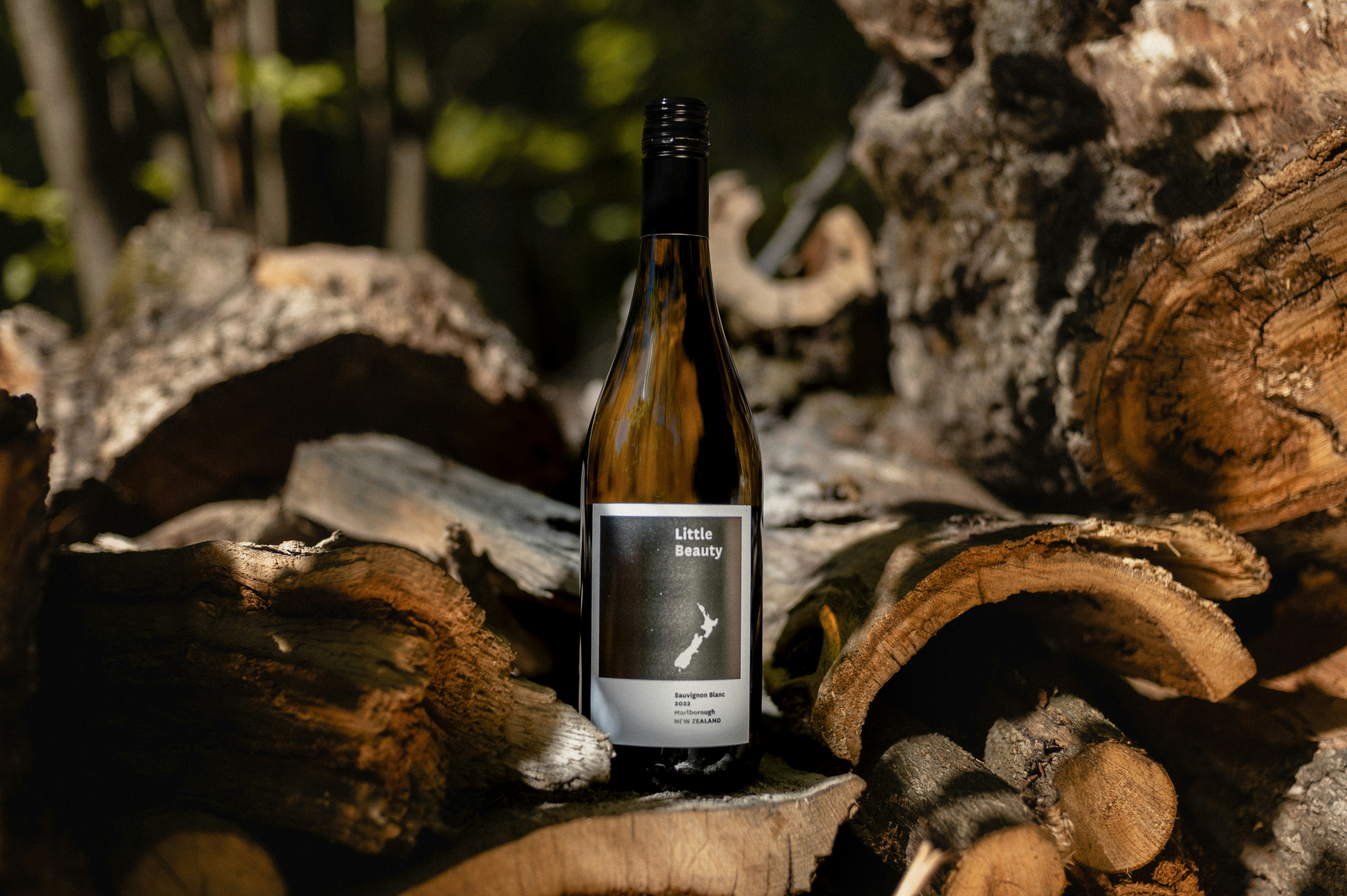 Bottle of Little Beauty nestled in warm, split logs