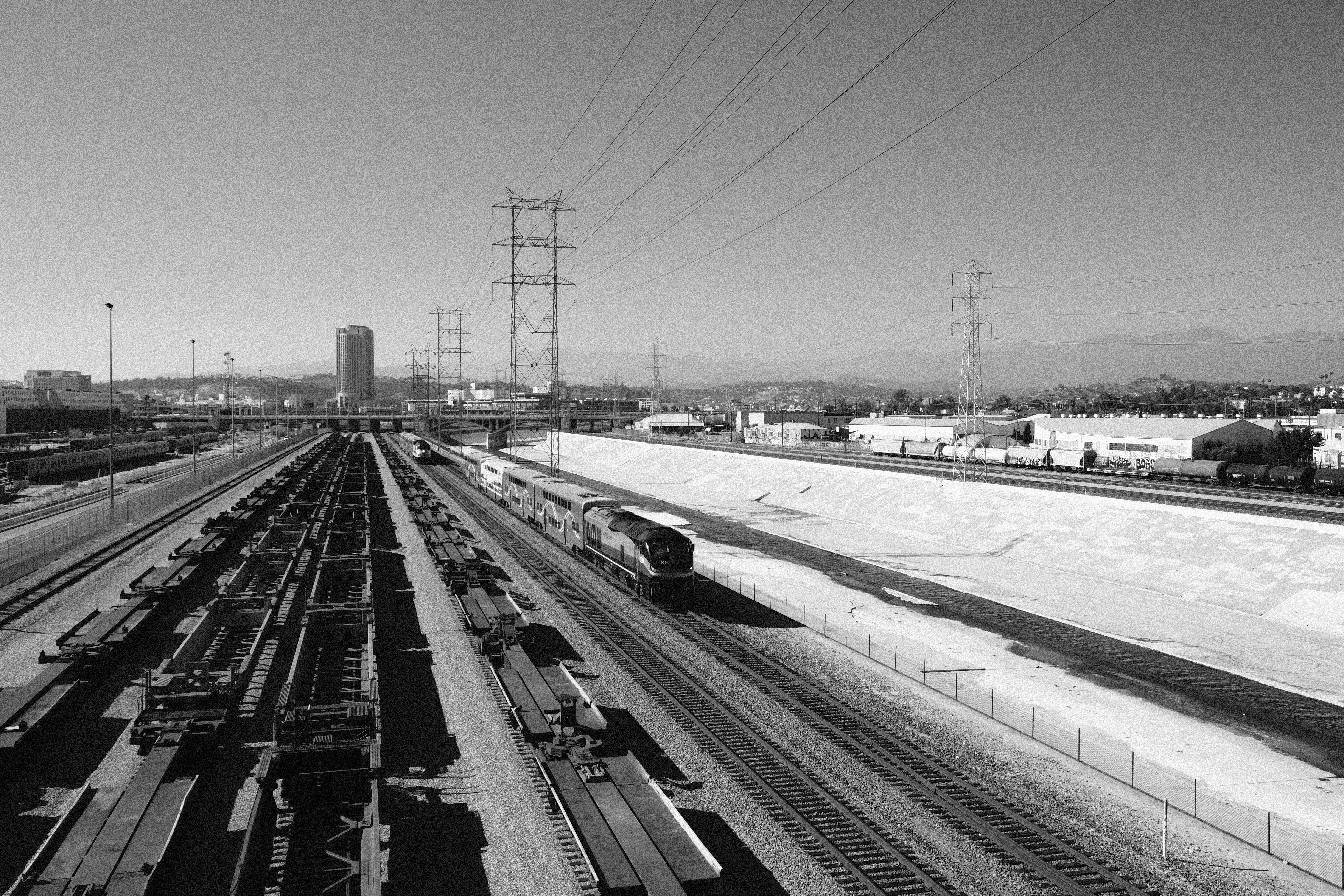 Black and white view of a train yard with parallel tracks and distant power lines under a clear sky.
