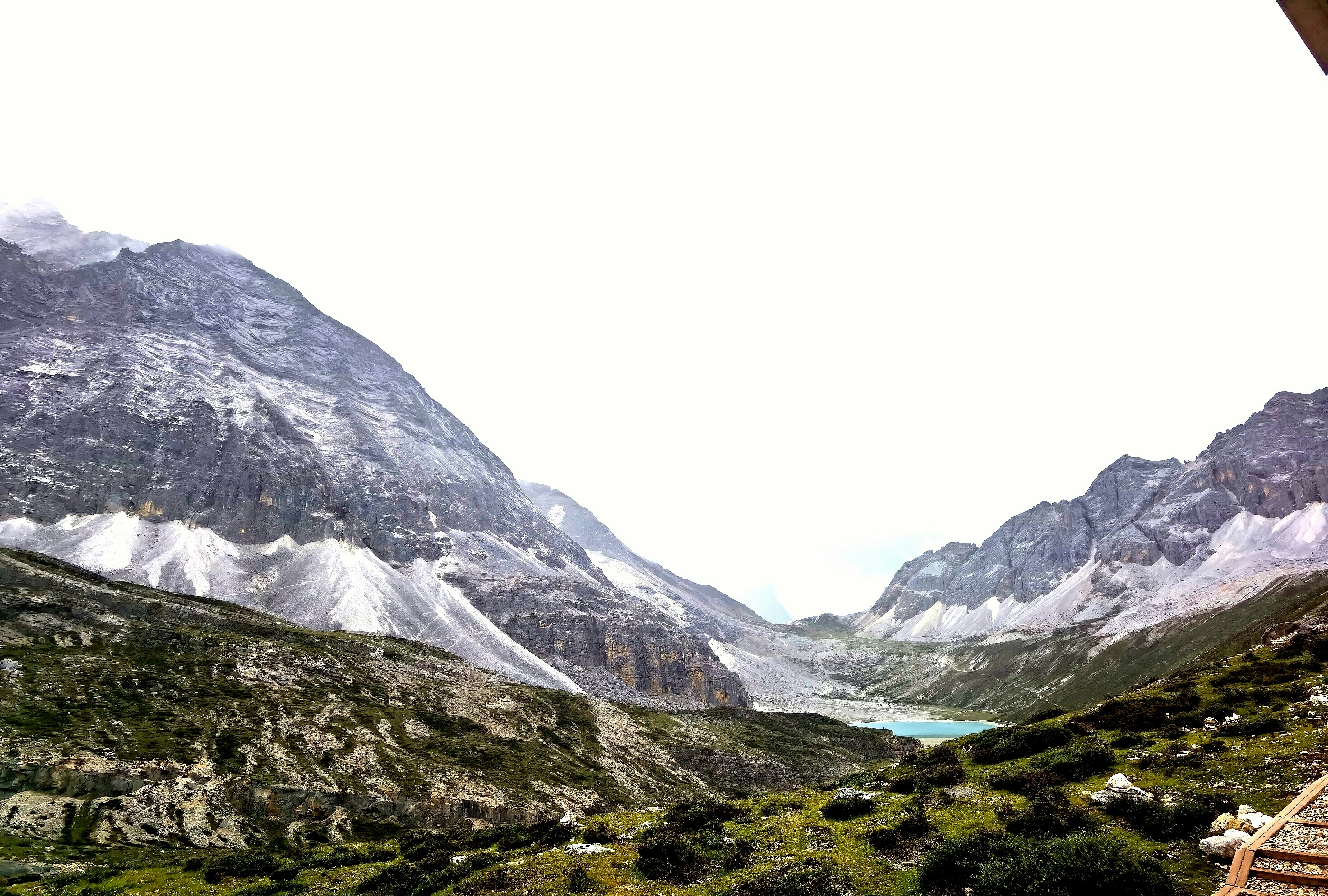 Glacier-carved valley reveals a turquoise alpine tarn, framed by rugged slopes and snow-dusted peaks.