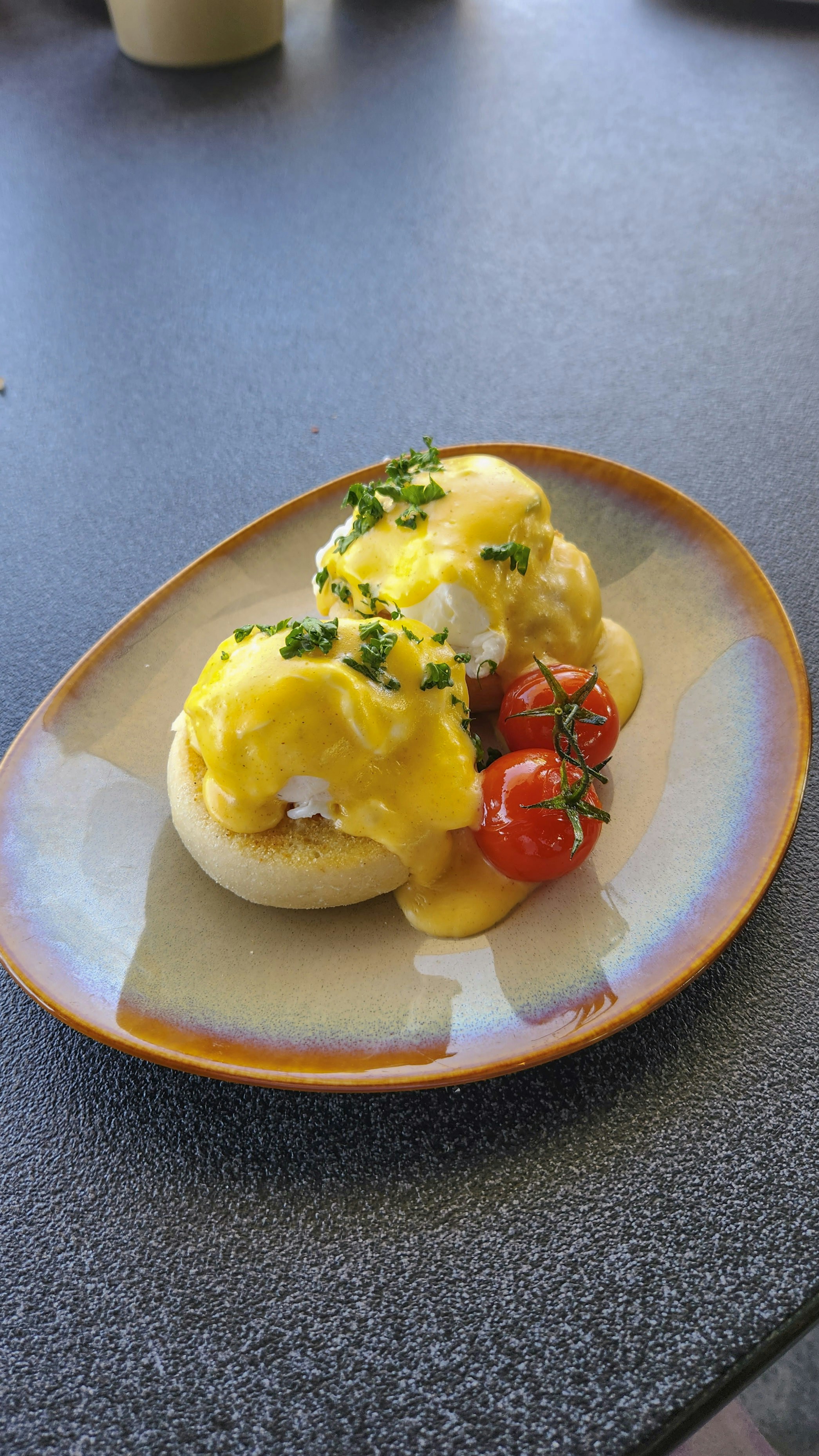 Sunny Hollandaise: Two Eggs Benedict on a Ceramic Plate with Vine-Ripe Tomatoes