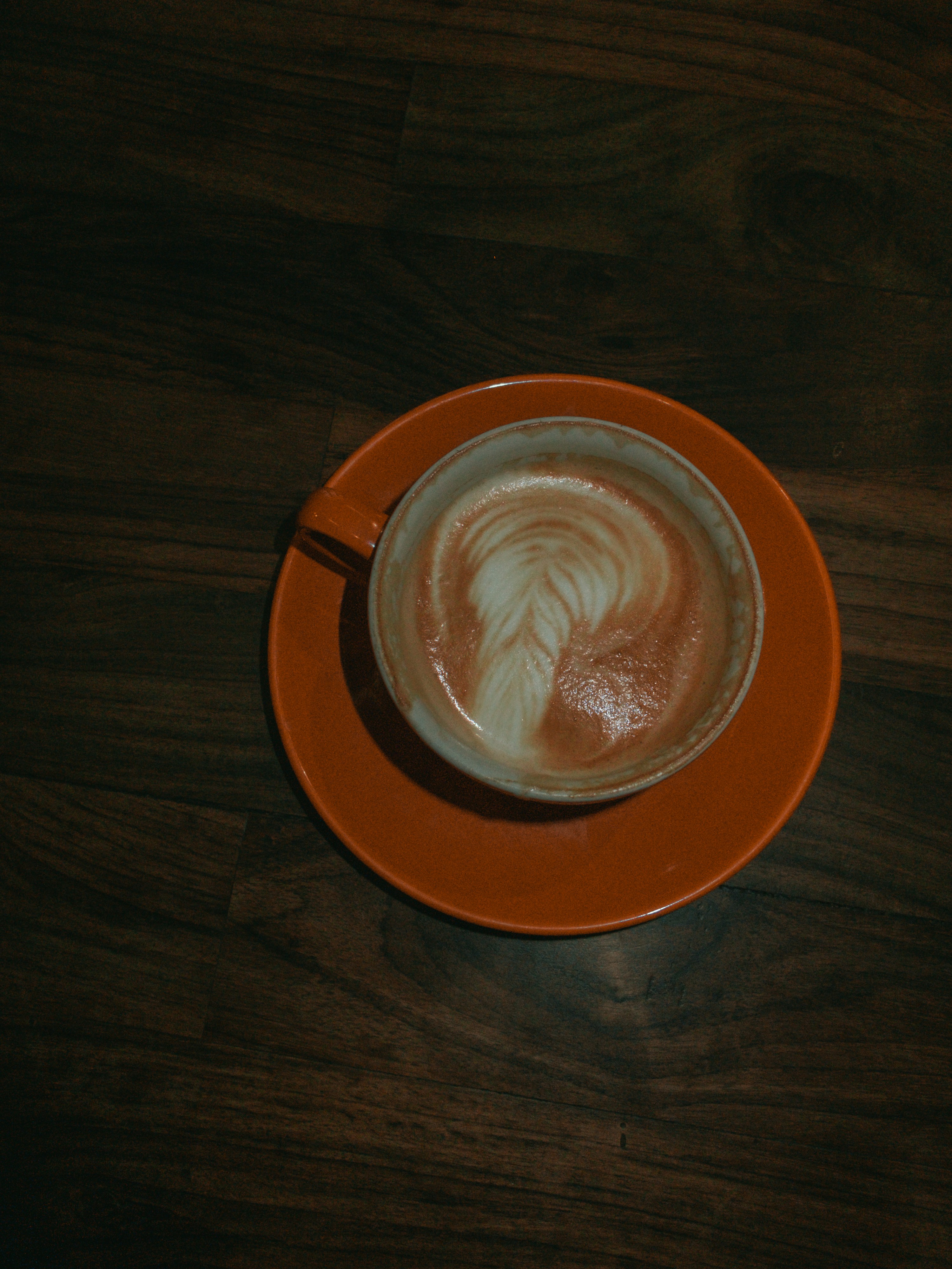 Top-down photograph of a latte with a rosette pattern on an orange saucer, set on a dark wooden table.