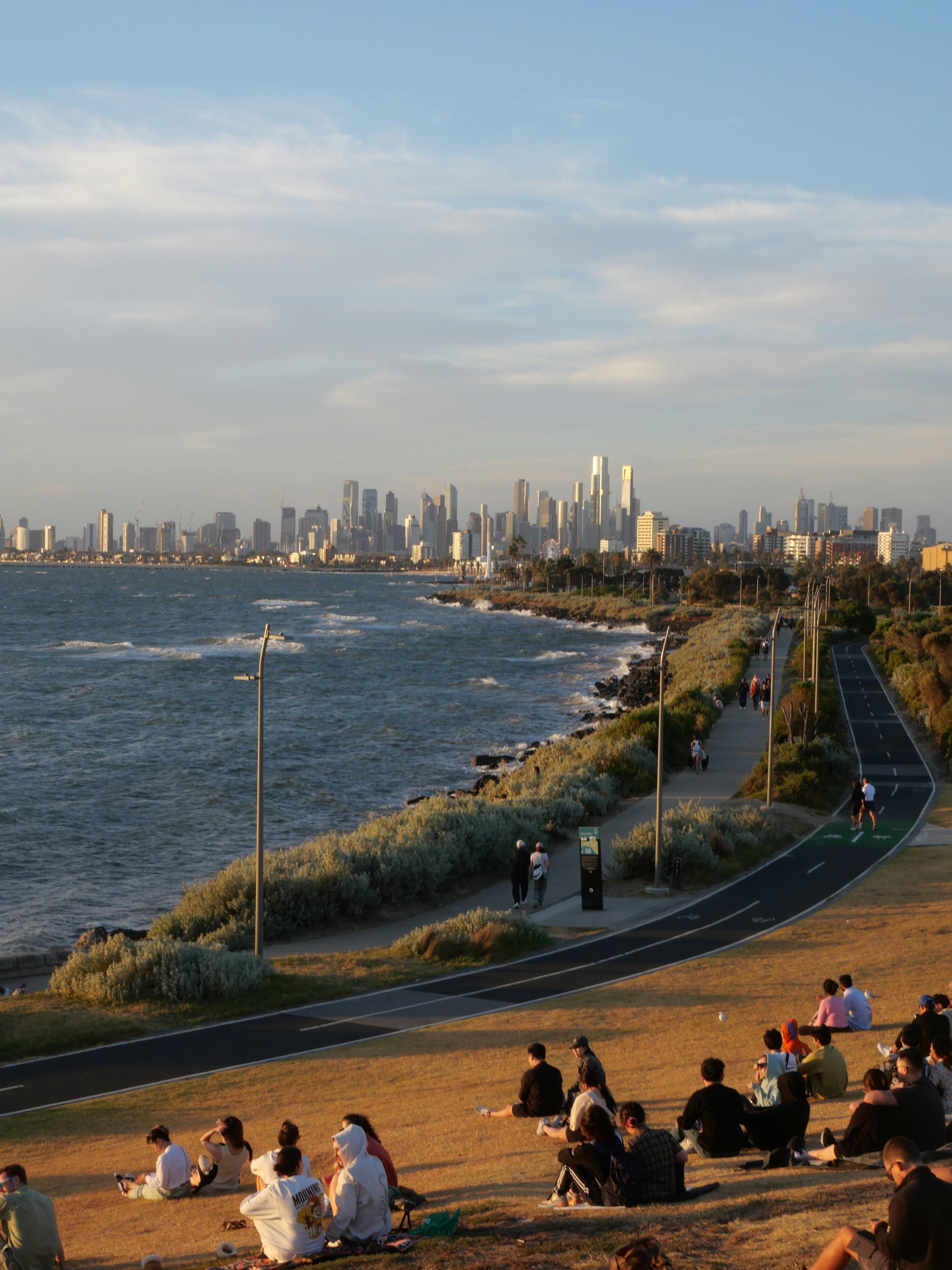 Cityscape meeting the coastline: sunlit promenade and gathering on the hill