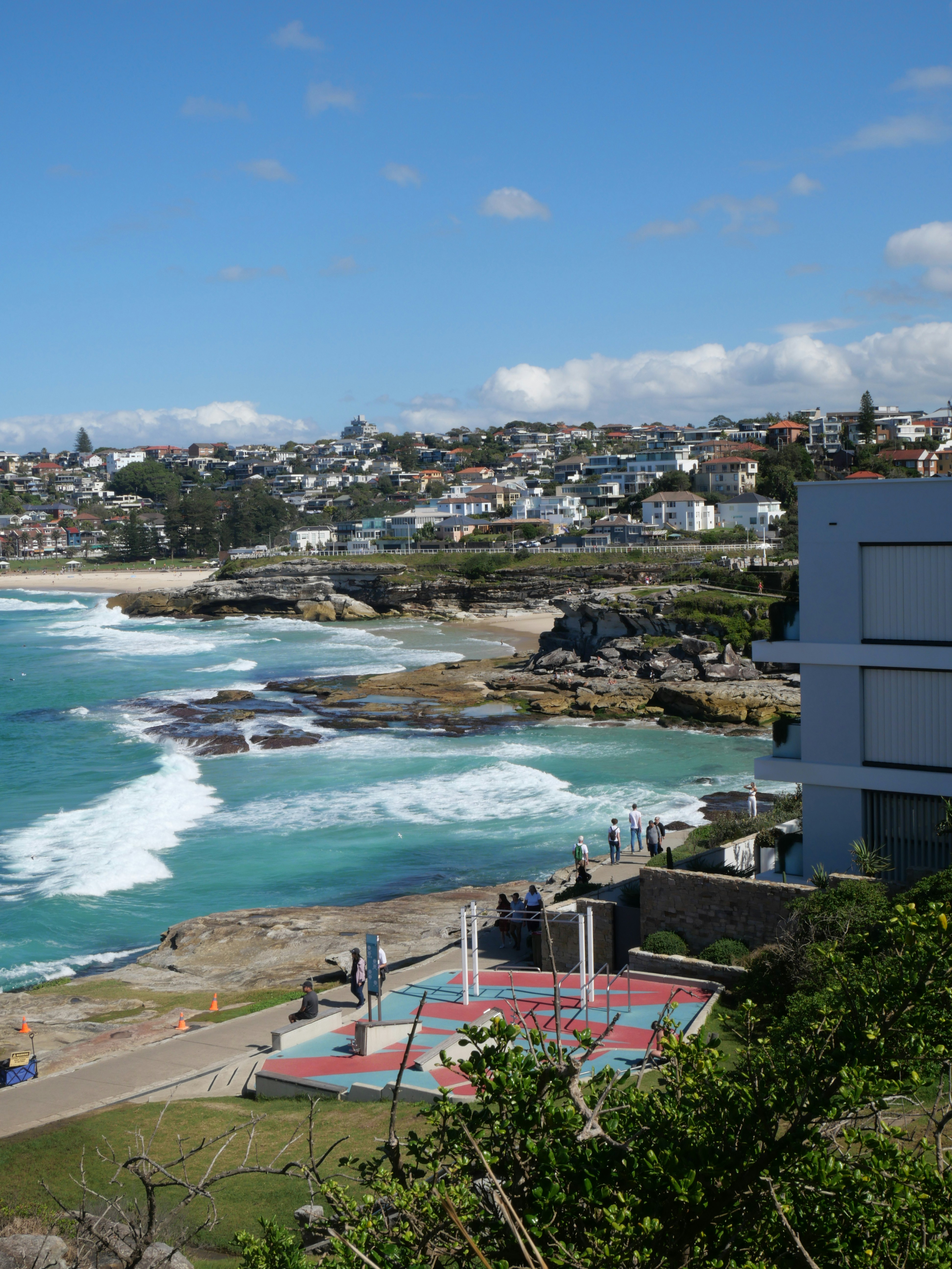 Vibrant coastal scene featuring a beach, rocky shoreline, and a colorful recreational area, with people enjoying the outdoors under a clear blue sky.