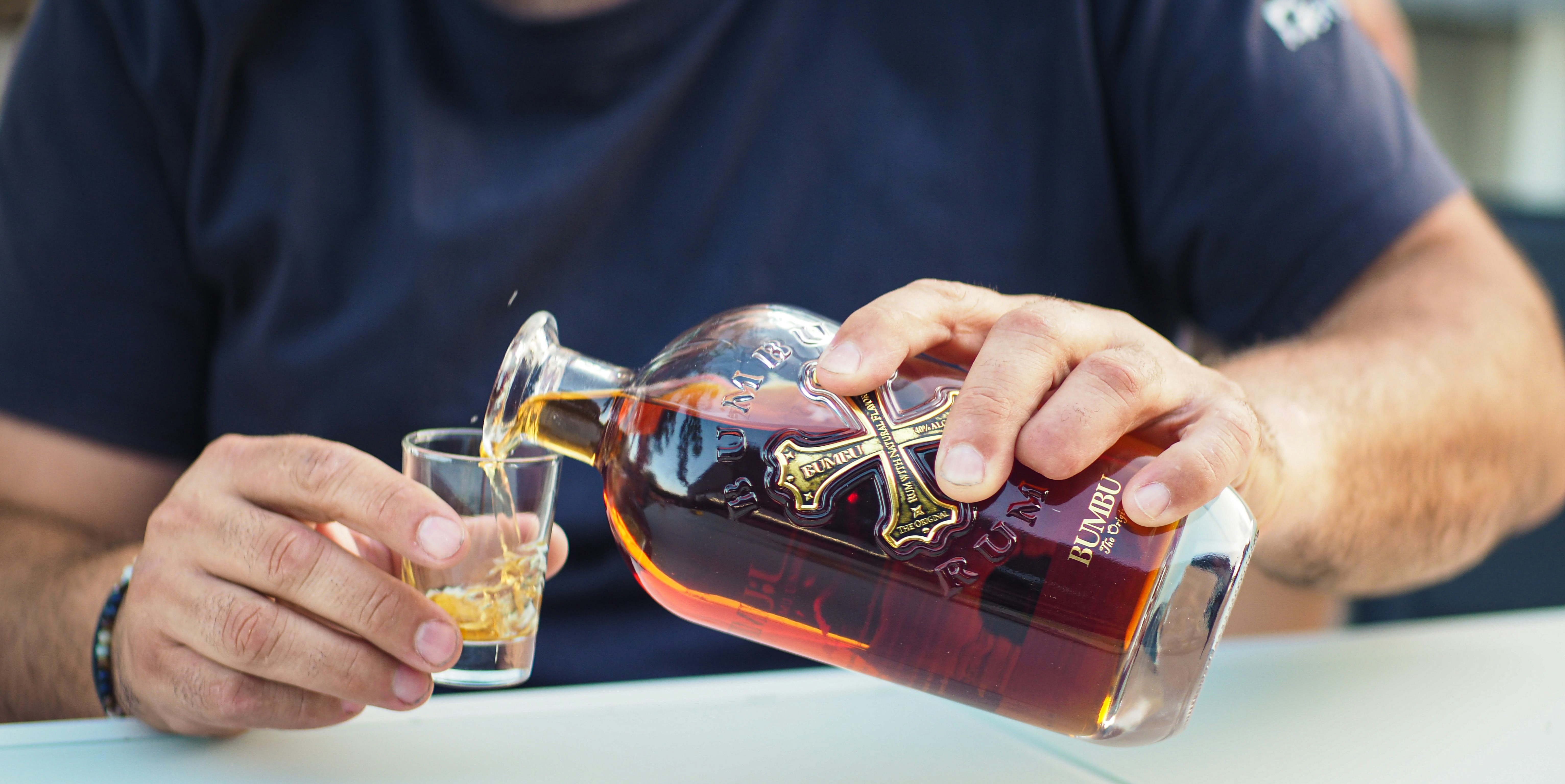 A dynamic moment of rum being poured into a glass, capturing the golden essence of the spirit as it splashes gently. The action conveys a sense of anticipation and the rich aroma of aged rum, perfect for illustrating articles or content about high-quality spirits and the culture of drinking well. | a man pouring a drink into a glass