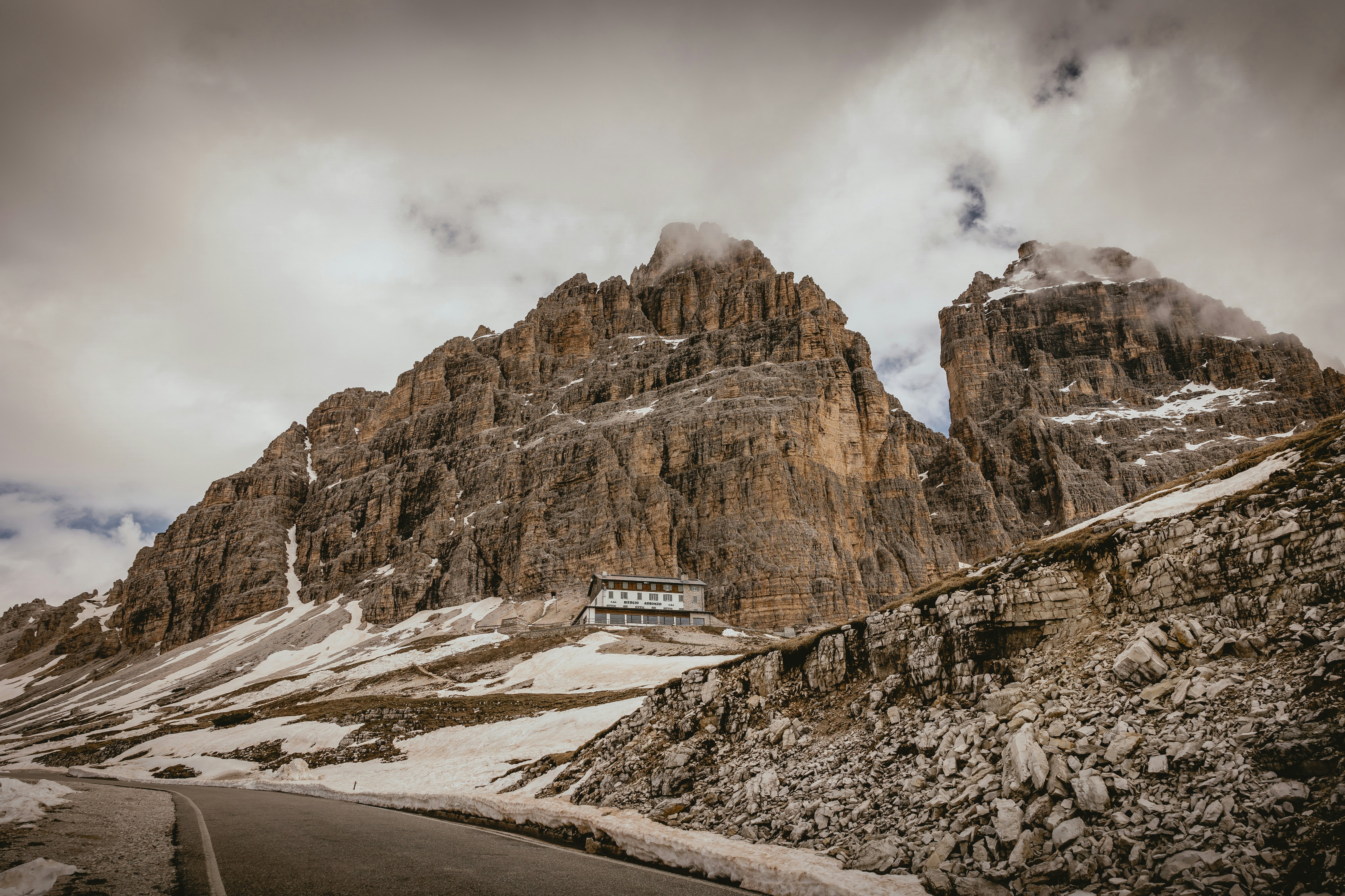 Mountain lodge nestled against rugged cliffs under a dramatic sky.
