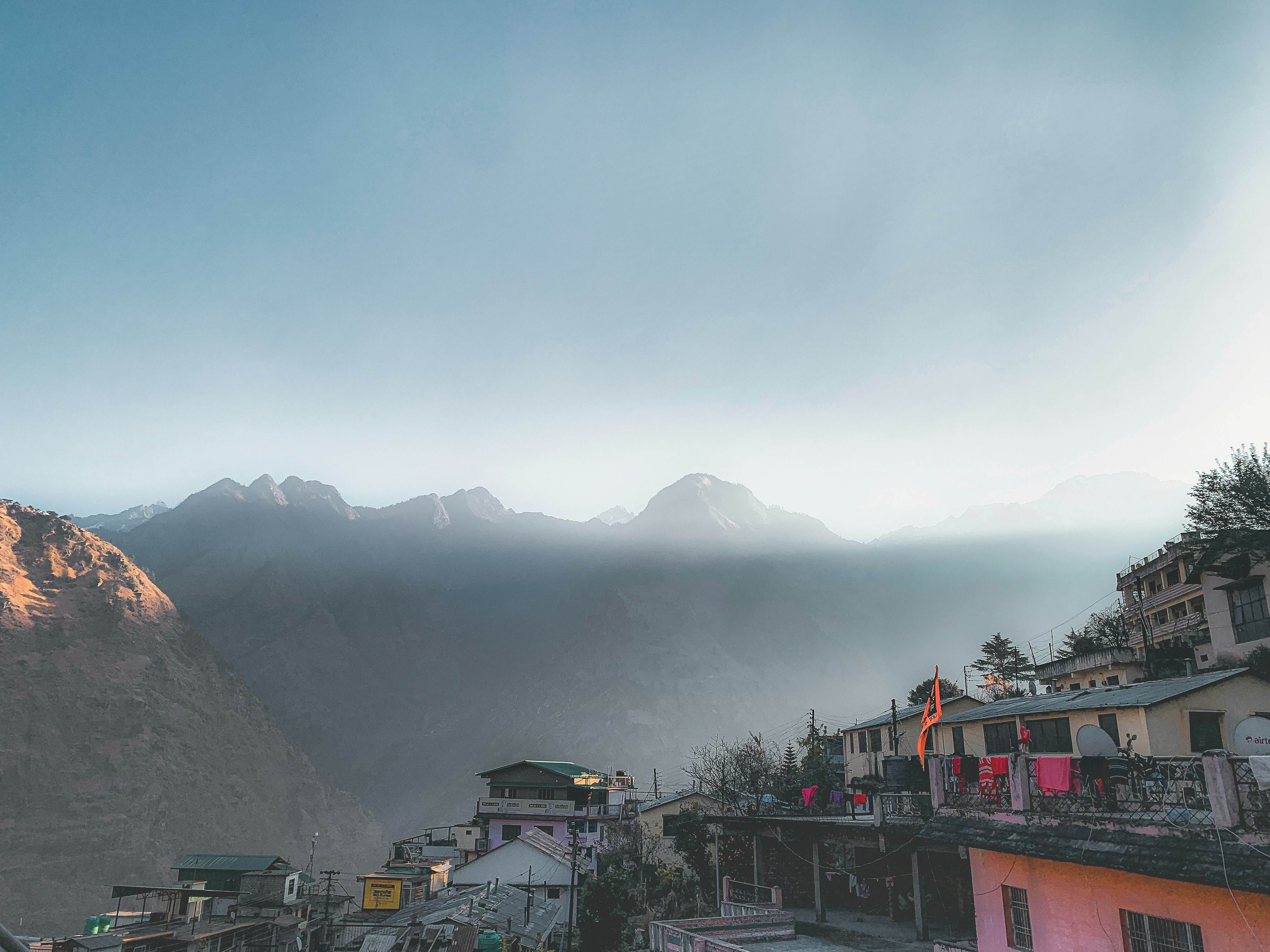 Distant mountains bathed in soft morning light with a village in the foreground under a clear sky.