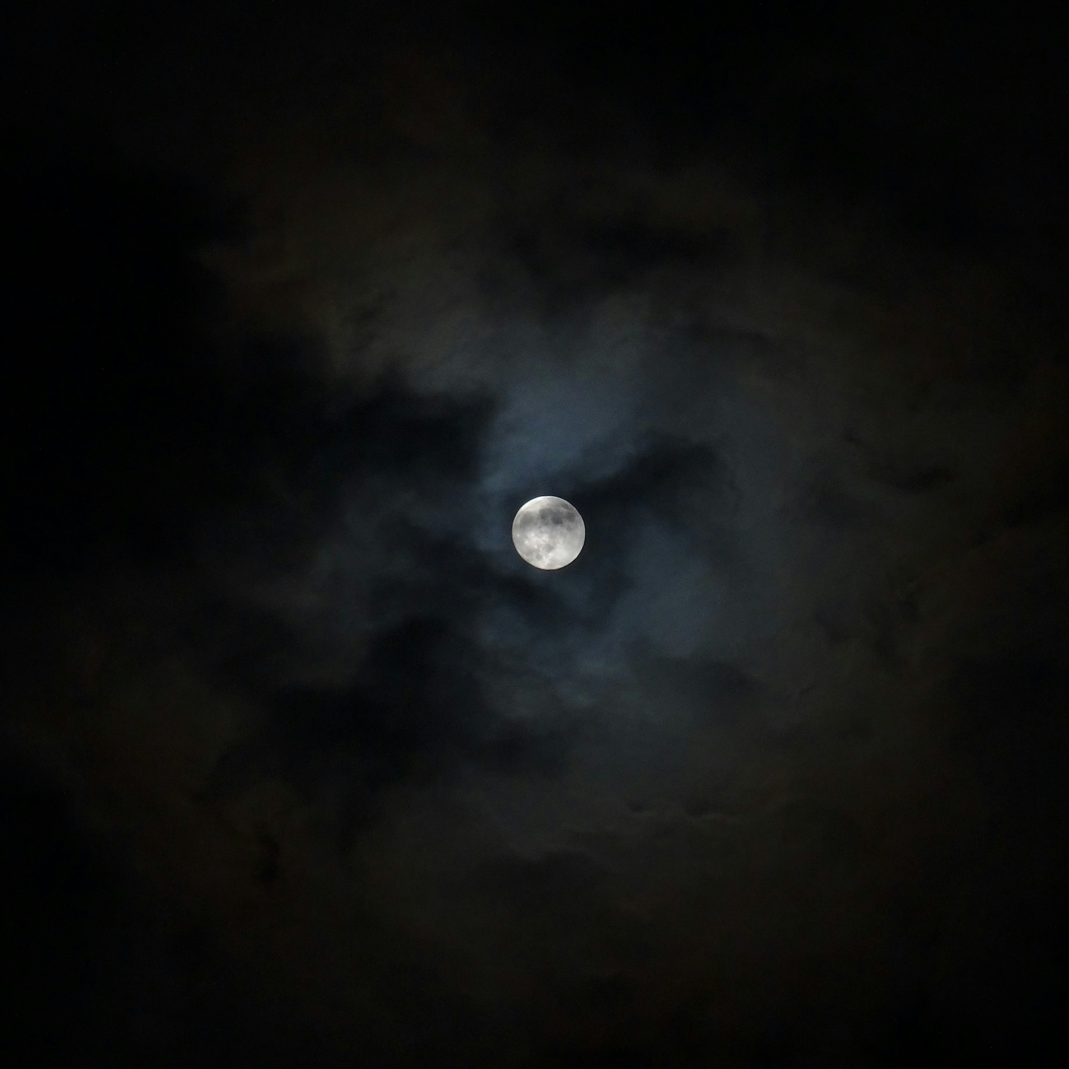 Full moon illuminating through scattered dark clouds at night.