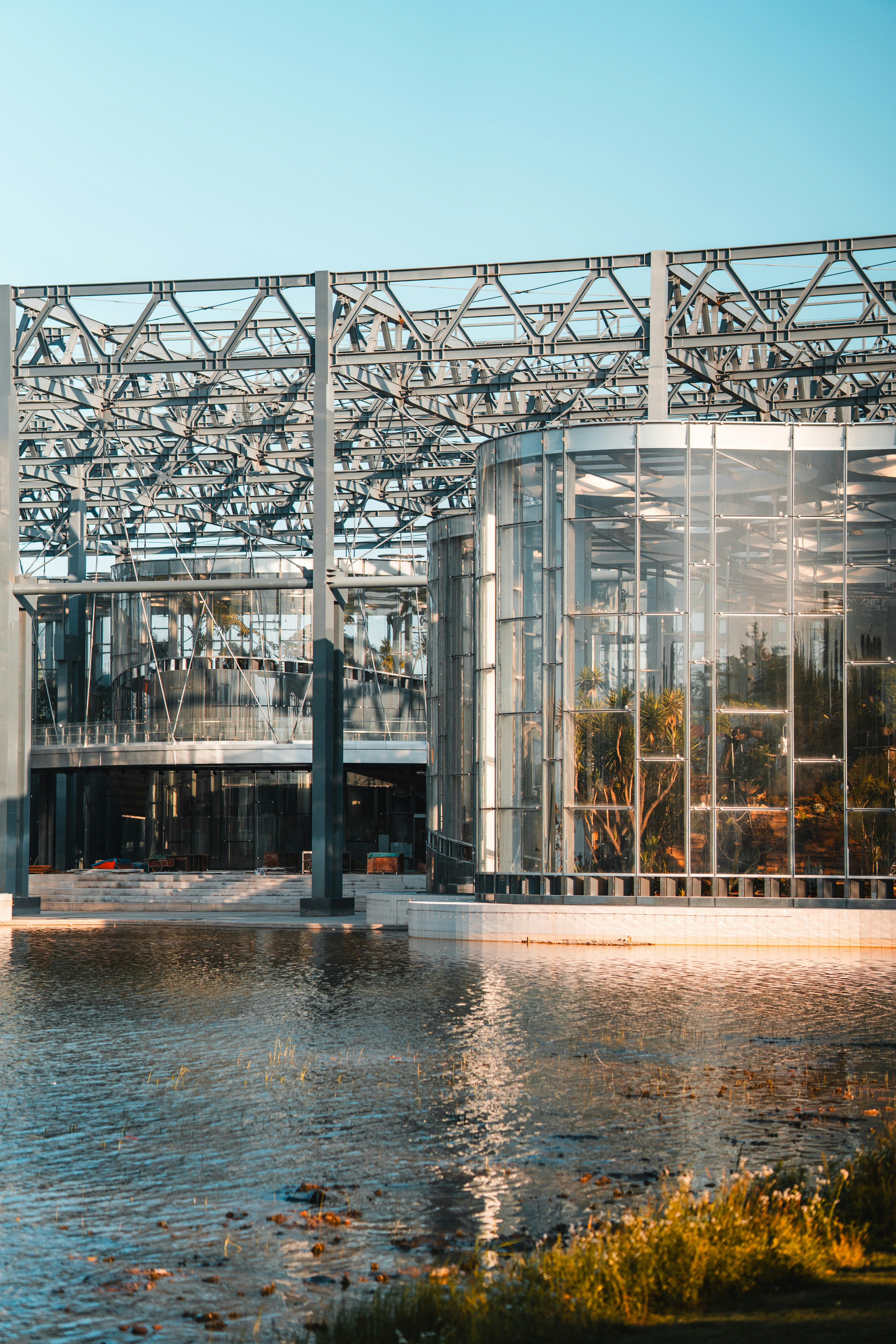 Glass Atrium Framed by Steel Lattice Over Calm Water