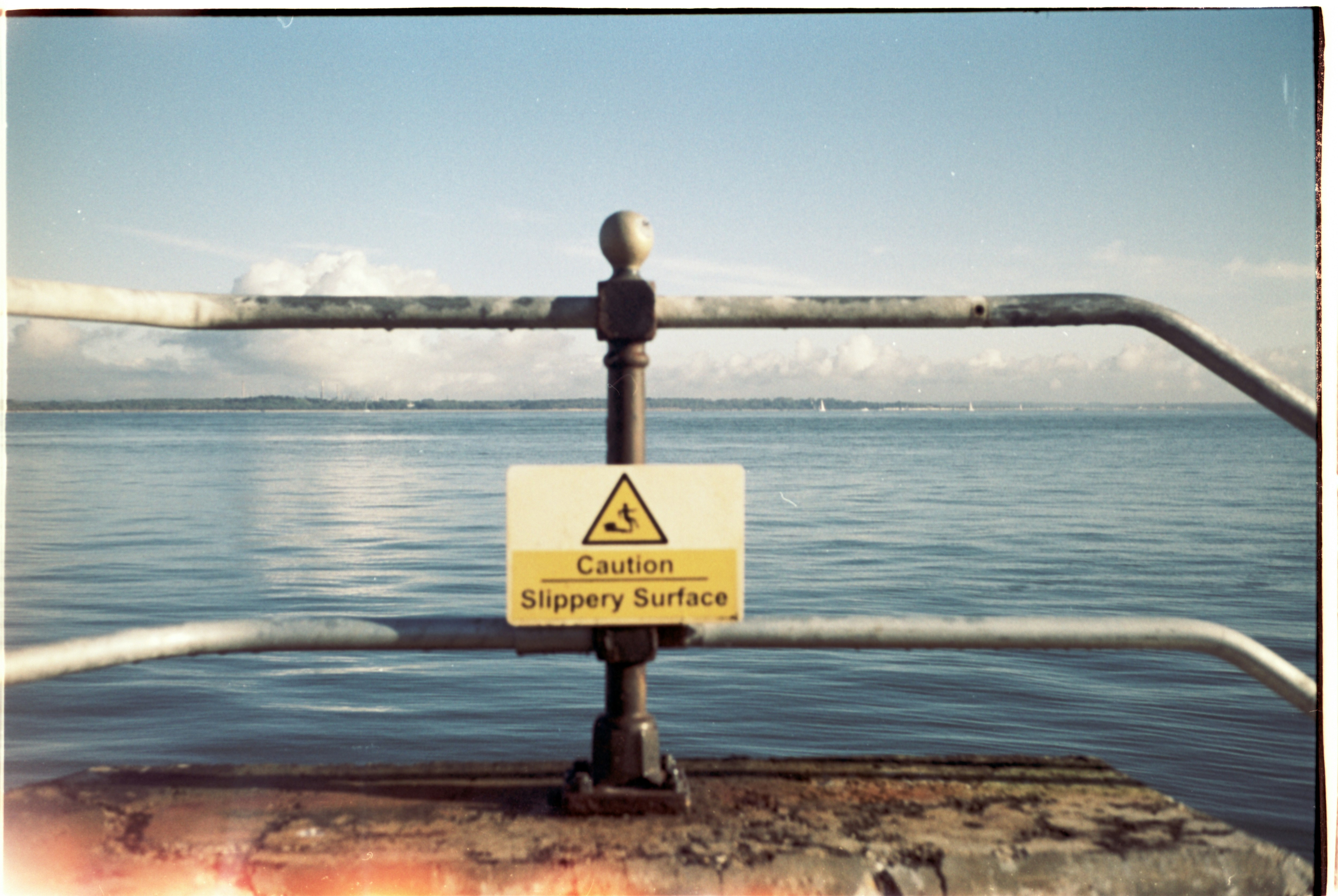A caution sign on a metal railing near the ocean photo – Free Analog ...