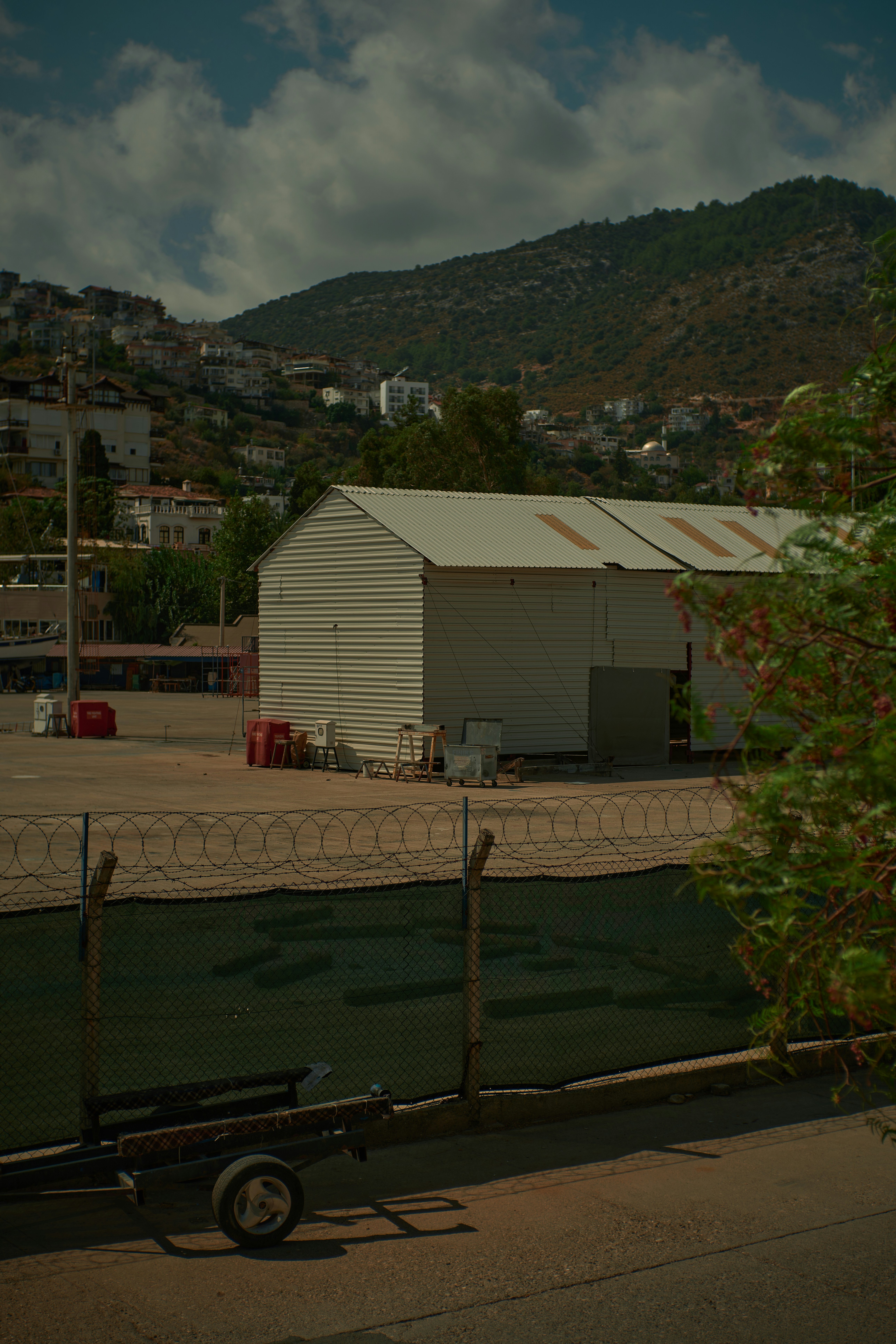A simple metallic structure stands in a quiet landscape, framed by rolling hills and a distant town. The scene captures a blend of human presence and natural beauty.