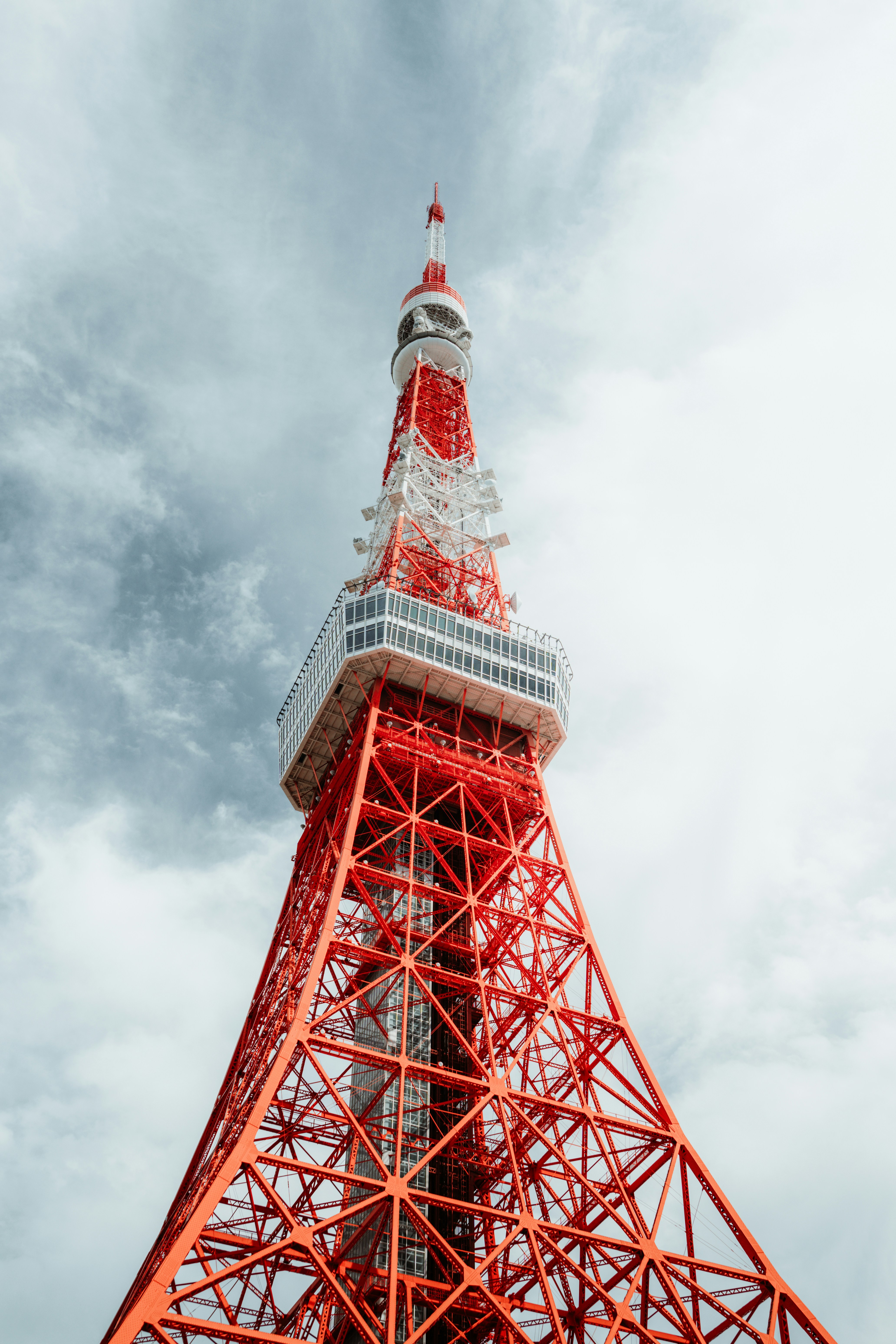 The Tokyo Tower rises majestically against a backdrop of dynamic clouds, showcasing its intricate red and white lattice structure.